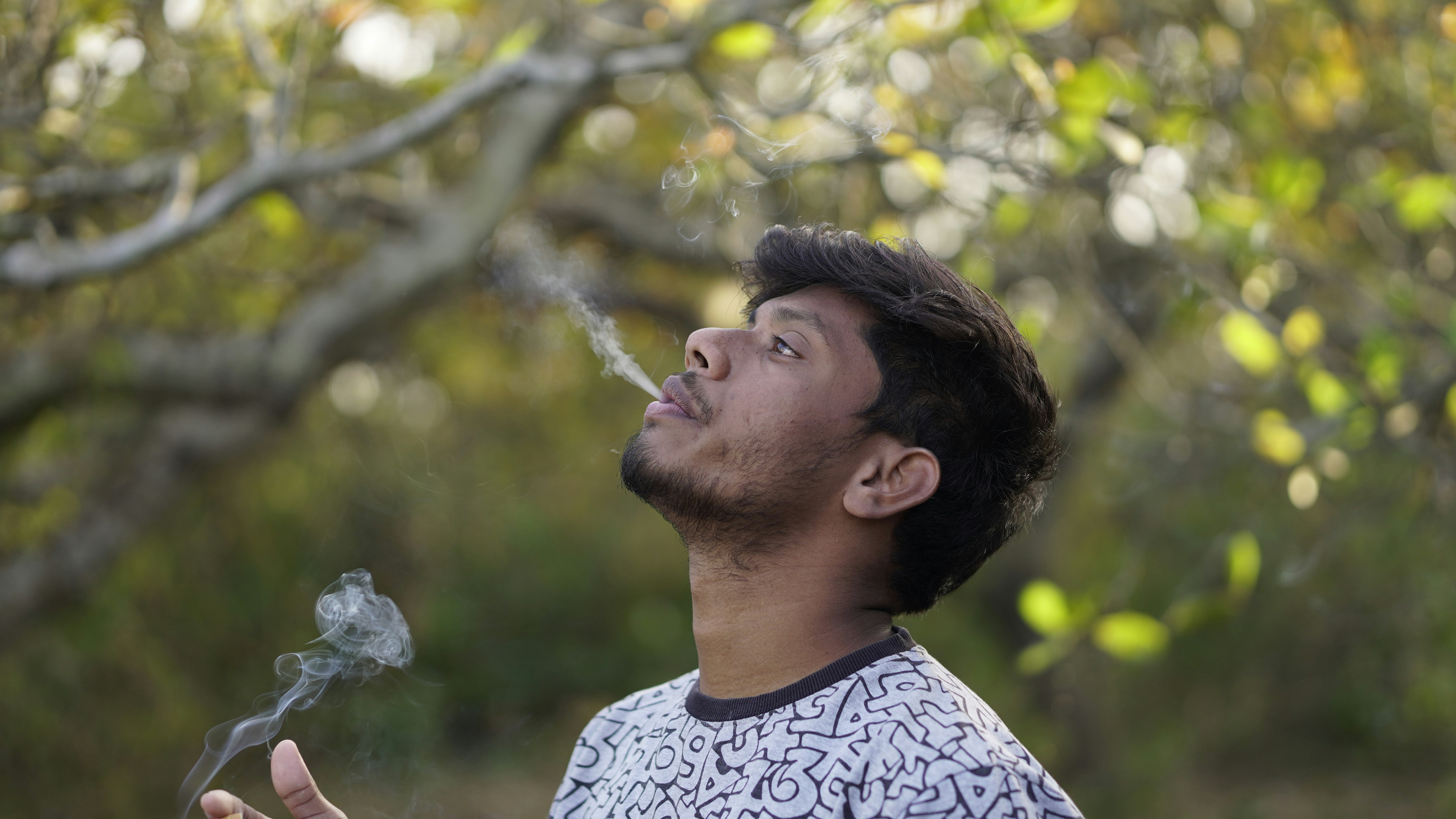 Un hombre está fumando un cigarrillo frente a un árbol foto – Imagen de ...