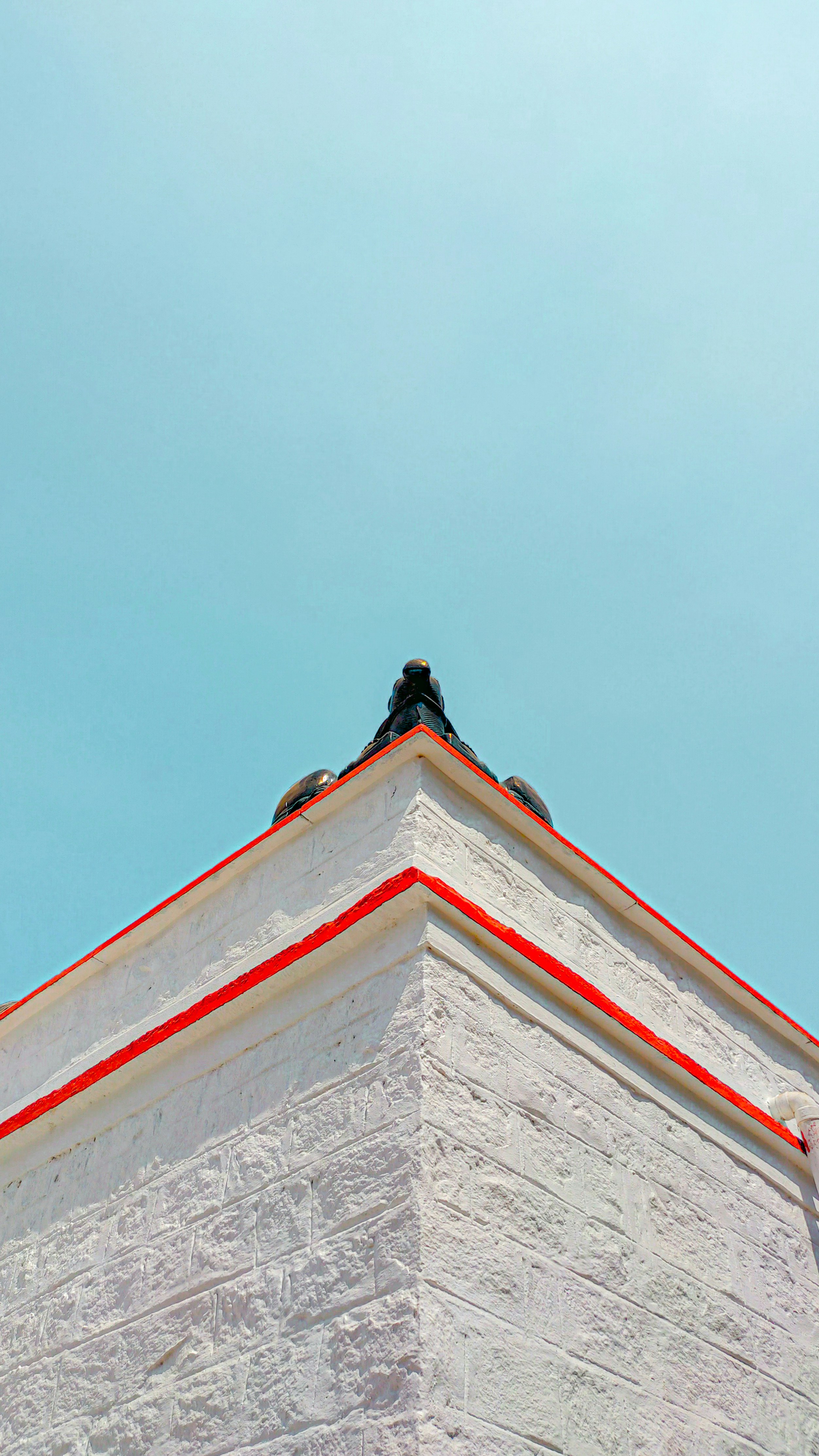 A close-up view of a building's corner, showcasing its textured white walls and vibrant red trim under a clear blue sky.
