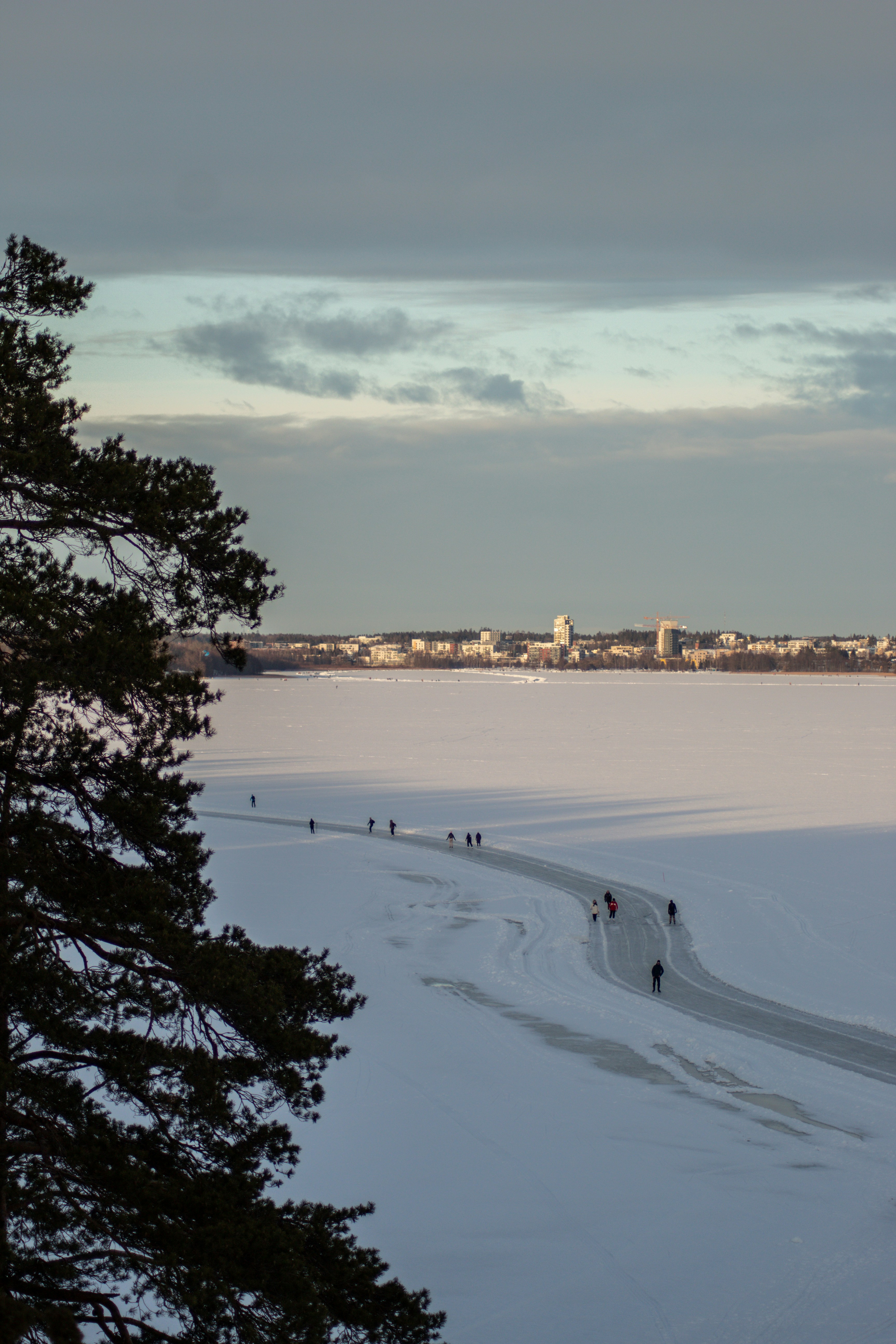 Snowbound Promenade: People Trek a Frosted Channel Toward a Distant Town