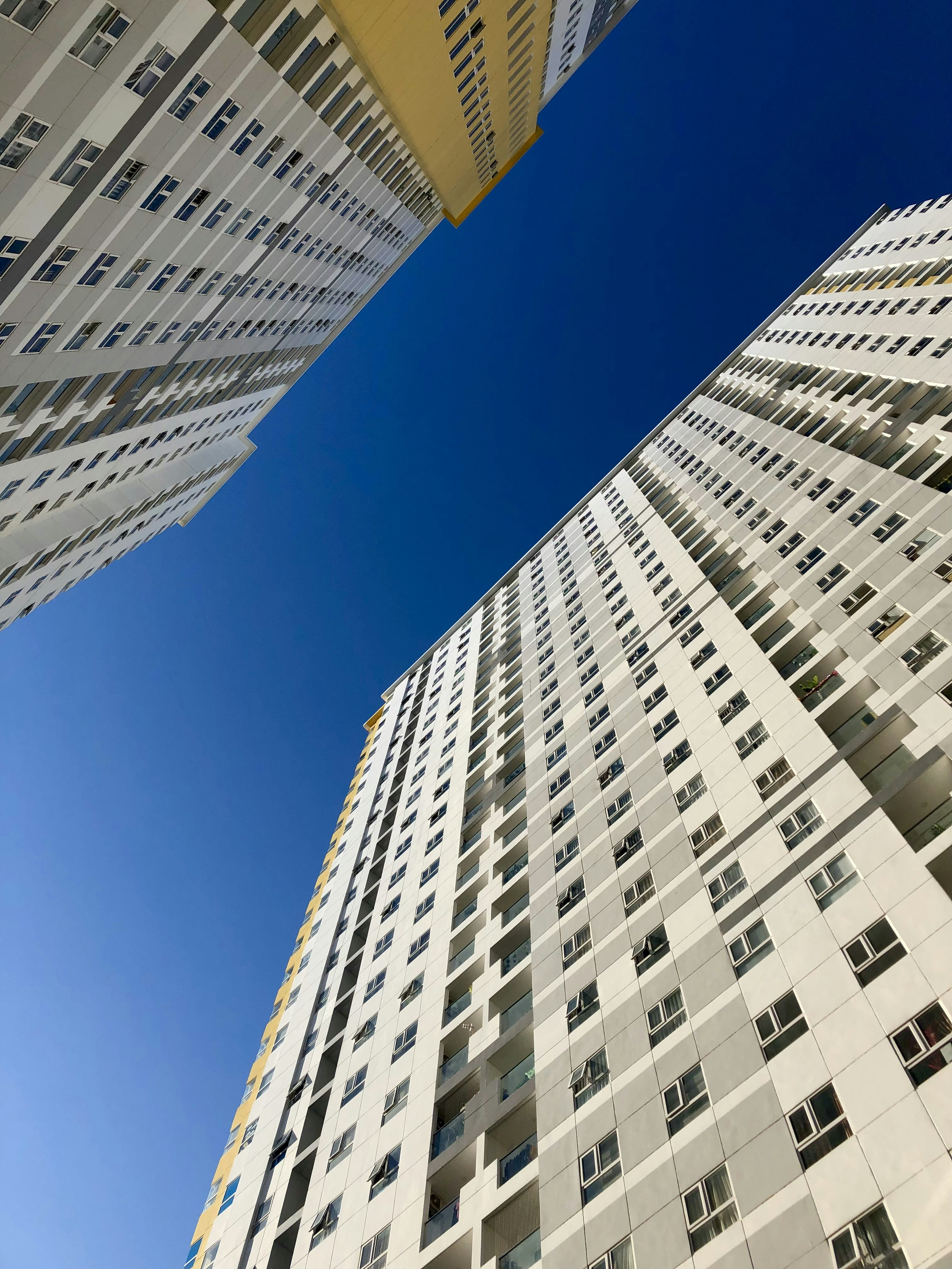 Tall residential buildings converge towards a clear blue sky, showcasing modern architectural lines and symmetry.