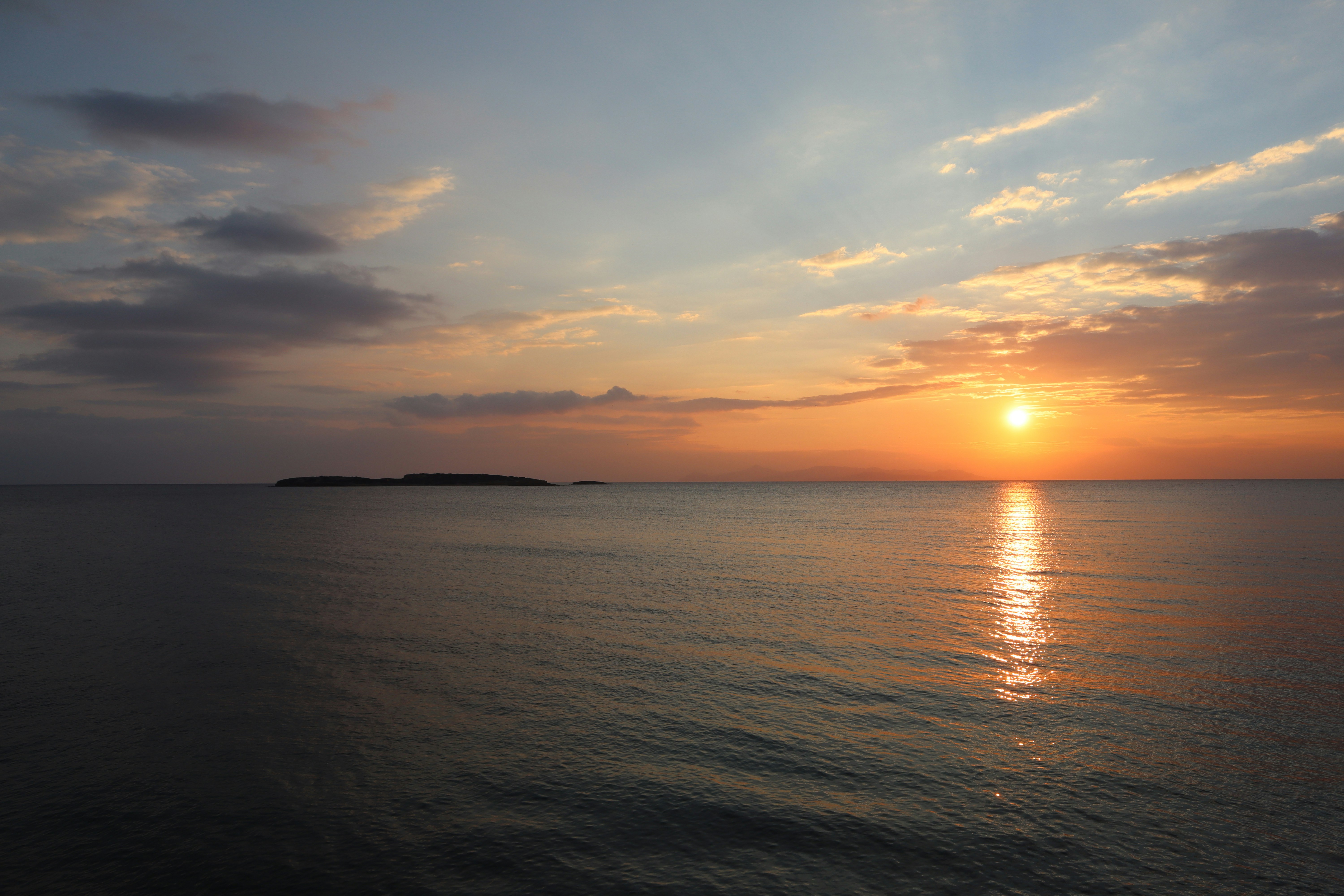 Golden sun setting over tranquil waters with distant island silhouette, creating a peaceful evening atmosphere.