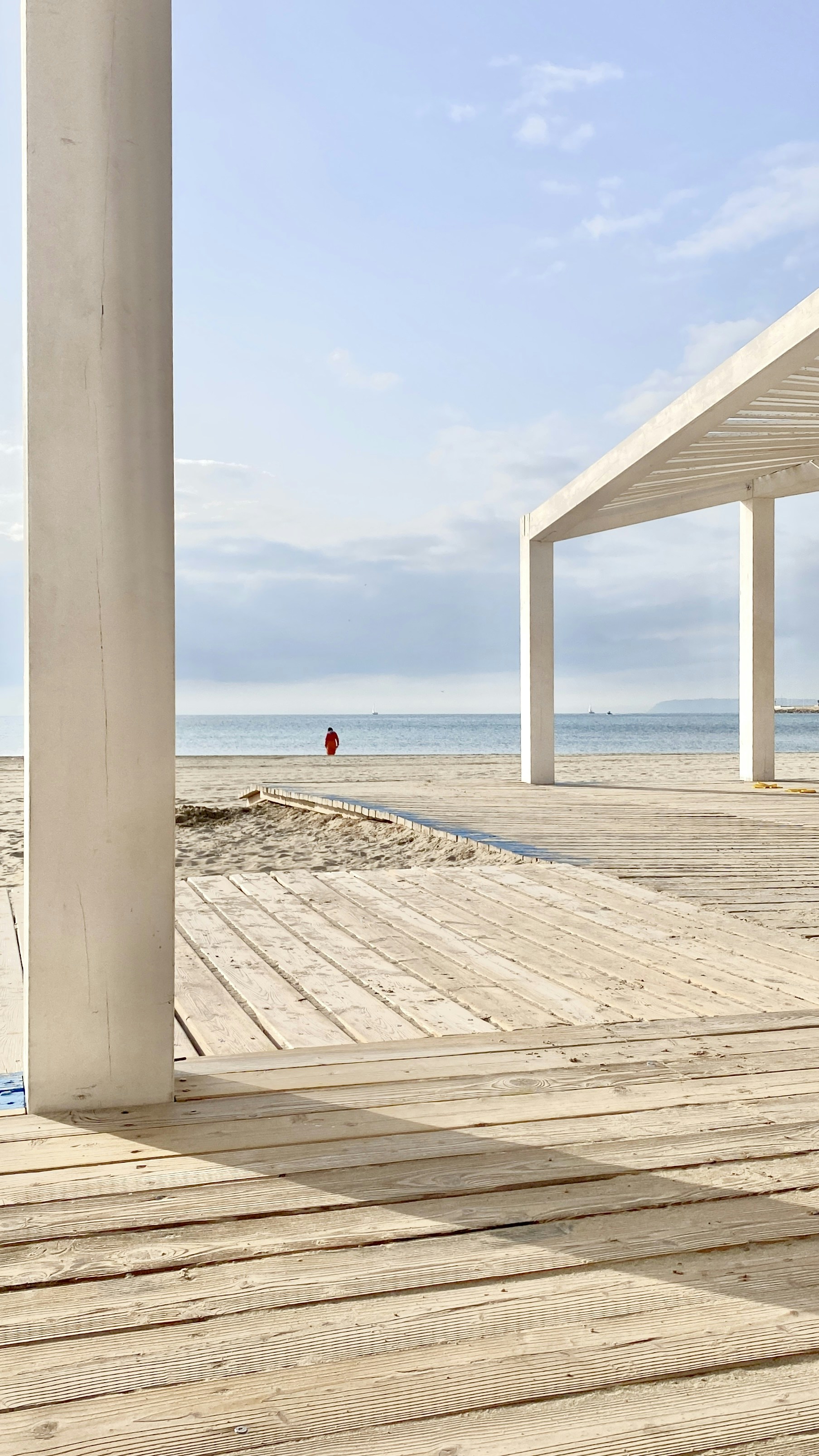Red Figure at the Quiet Beach Boardwalk Framed by Modern White Pergolas