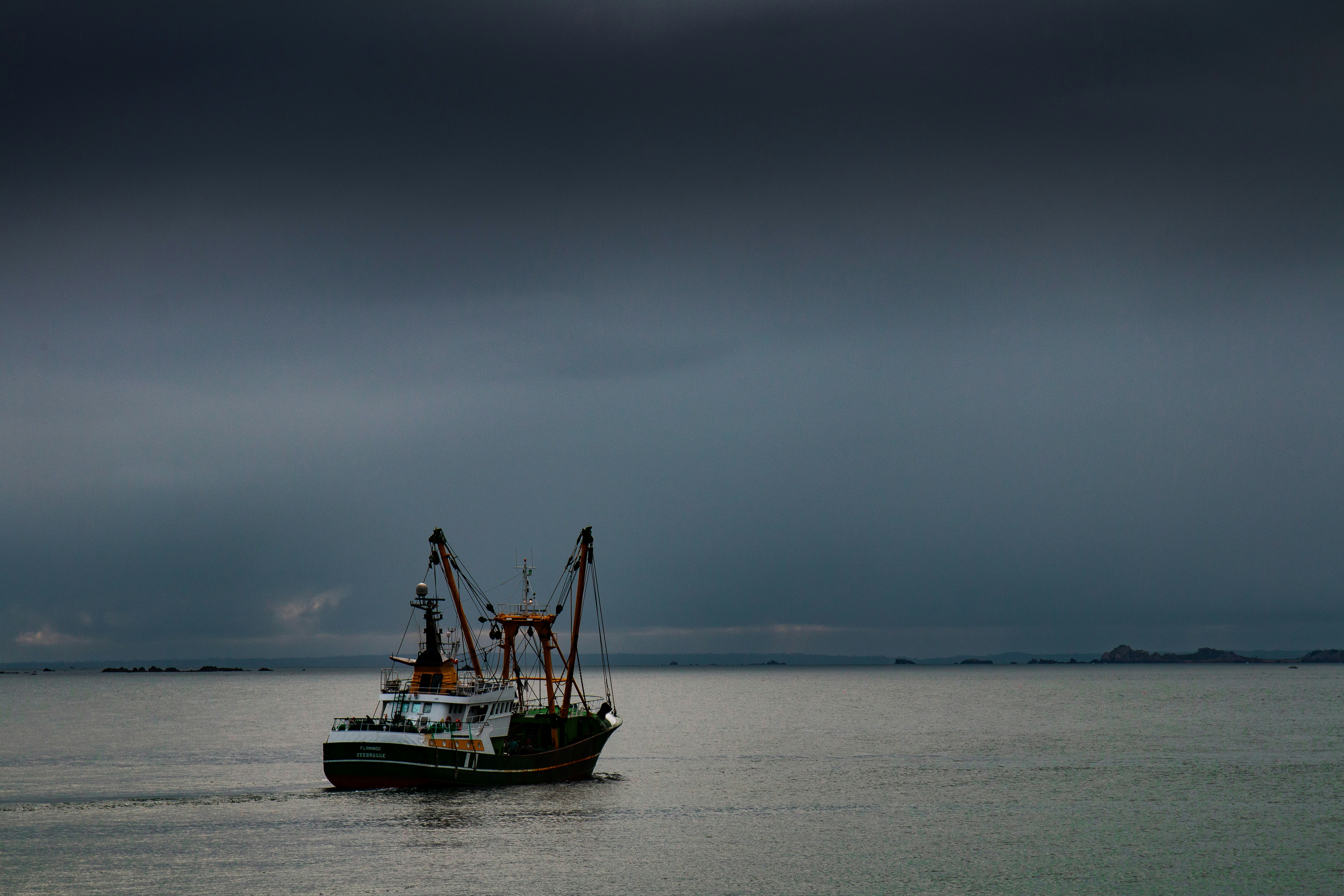 Fishing vessel navigating the calm waters under a moody sky, reflecting the tranquility and solitude of maritime life.