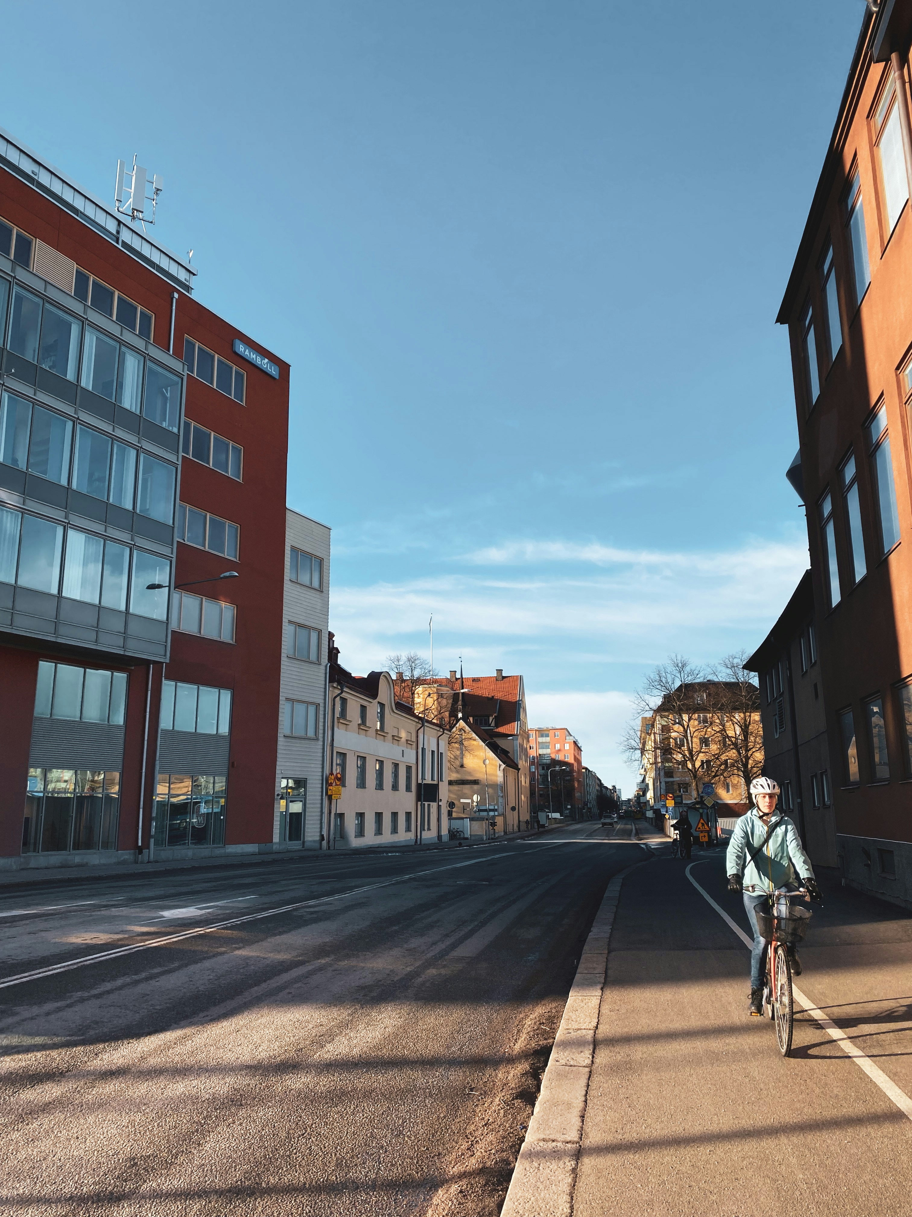 Cyclist riding along a city street flanked by modern buildings under a clear blue sky.