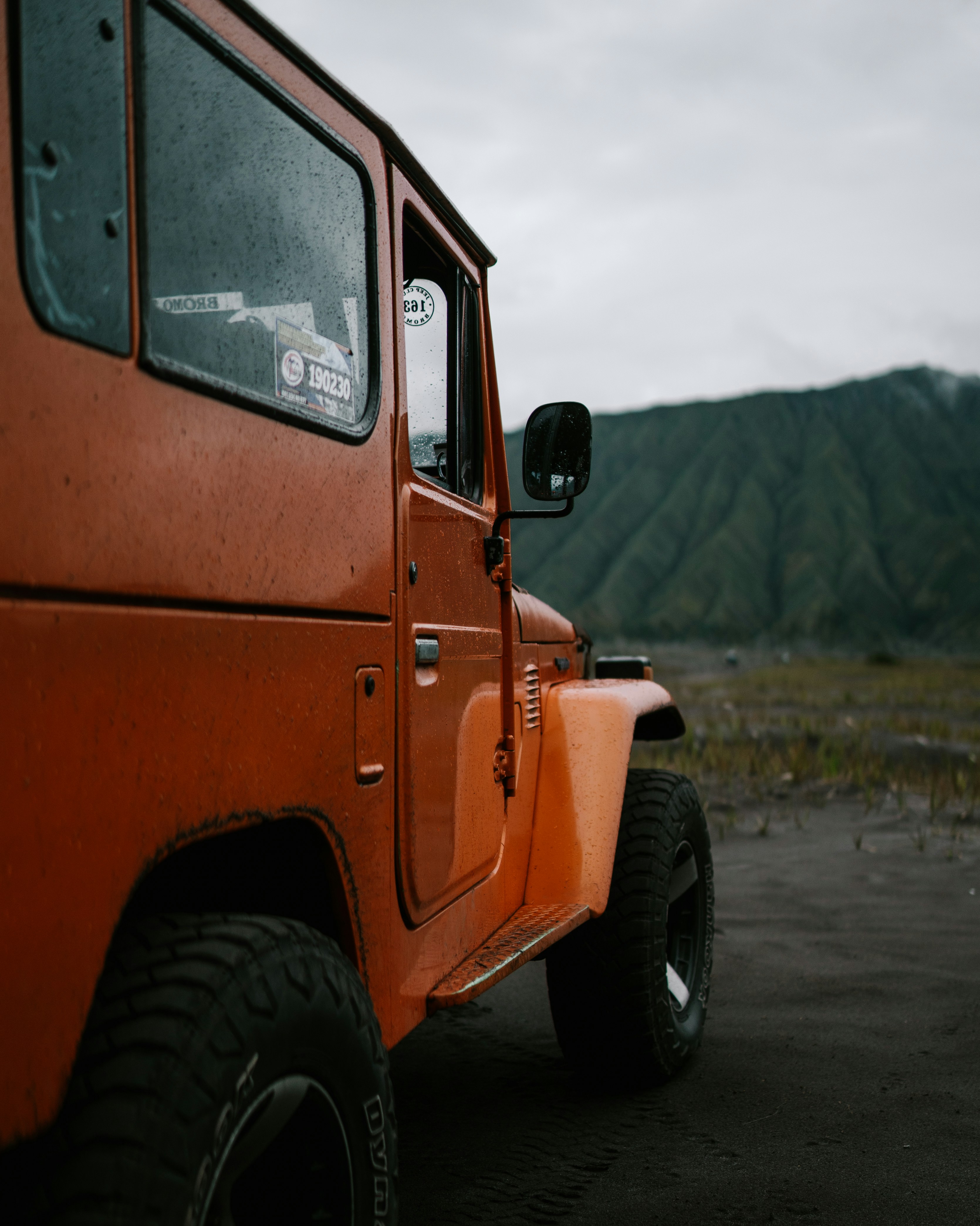 an orange jeep parked in a parking lot with mountains in the background