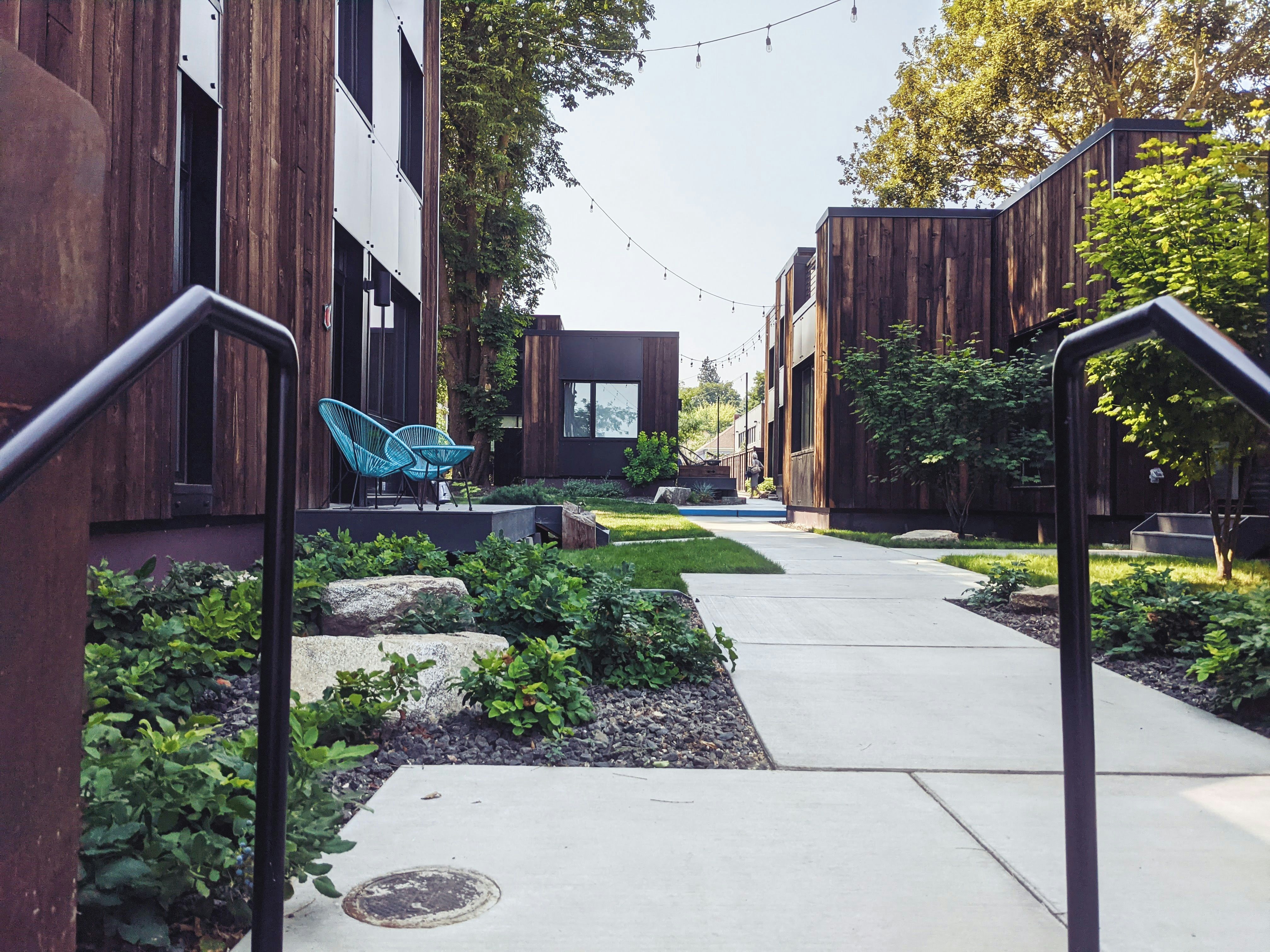 Pathway flanked by modern buildings and lush greenery under a clear sky.