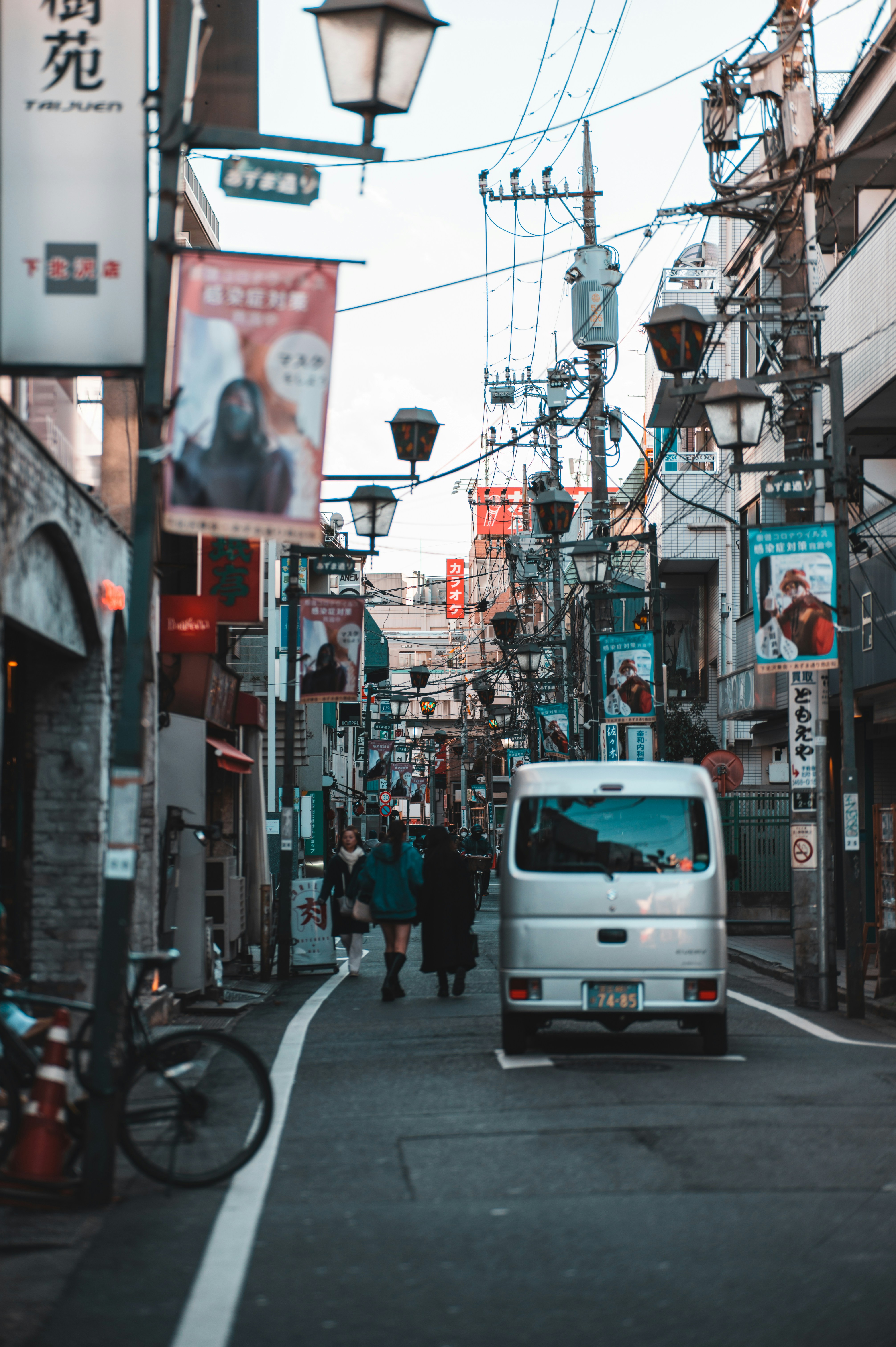 Narrow street bustling with pedestrians and vehicles, adorned with colorful banners and streetlights. A blend of modernity and tradition is evident in the urban landscape.