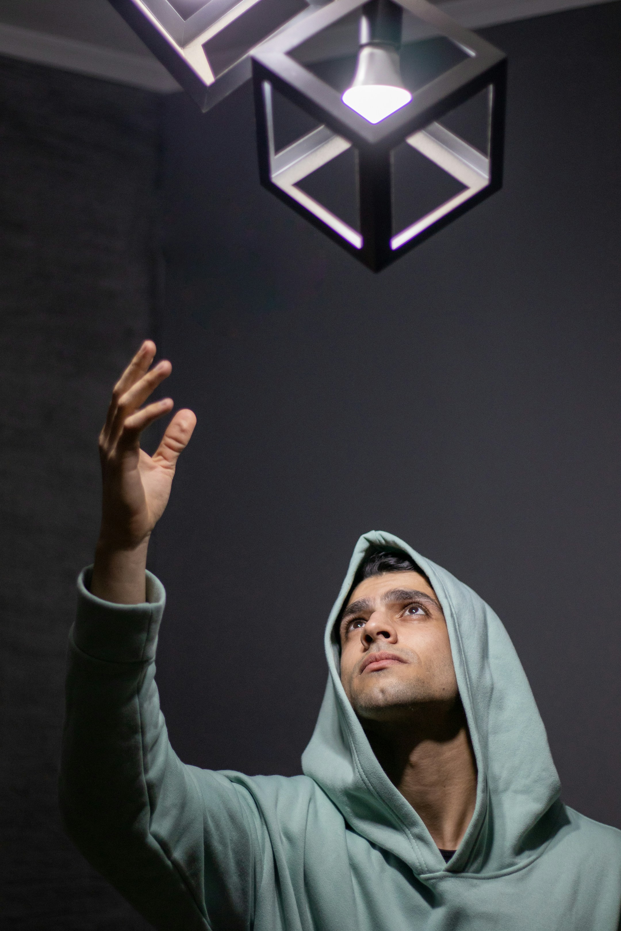A man in a hoodie reaching up to a light fixture photo – Free Person ...