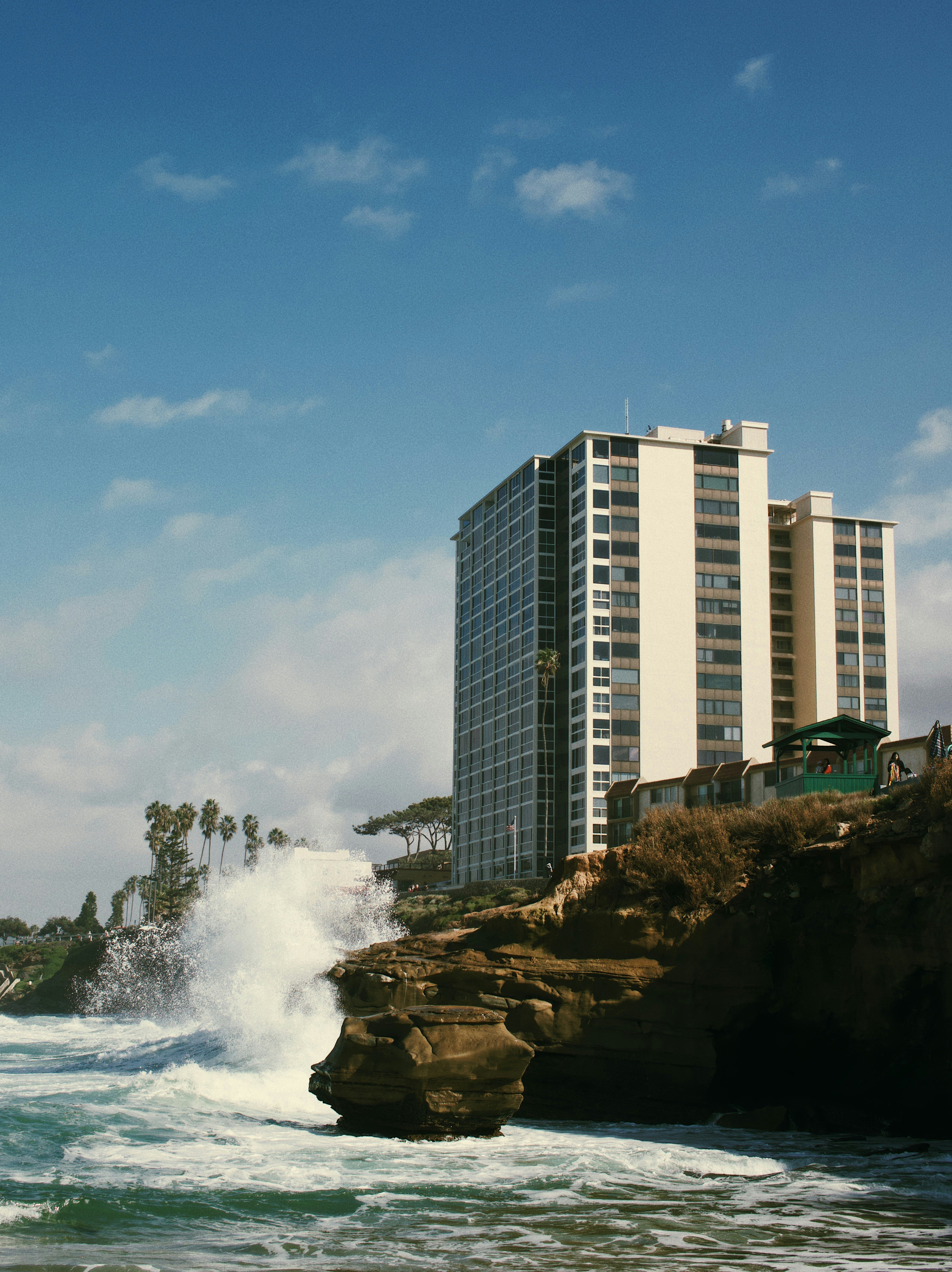 Ocean waves crashing against rocky coastline with a modern building in the background, capturing the dynamic interplay of nature and architecture.