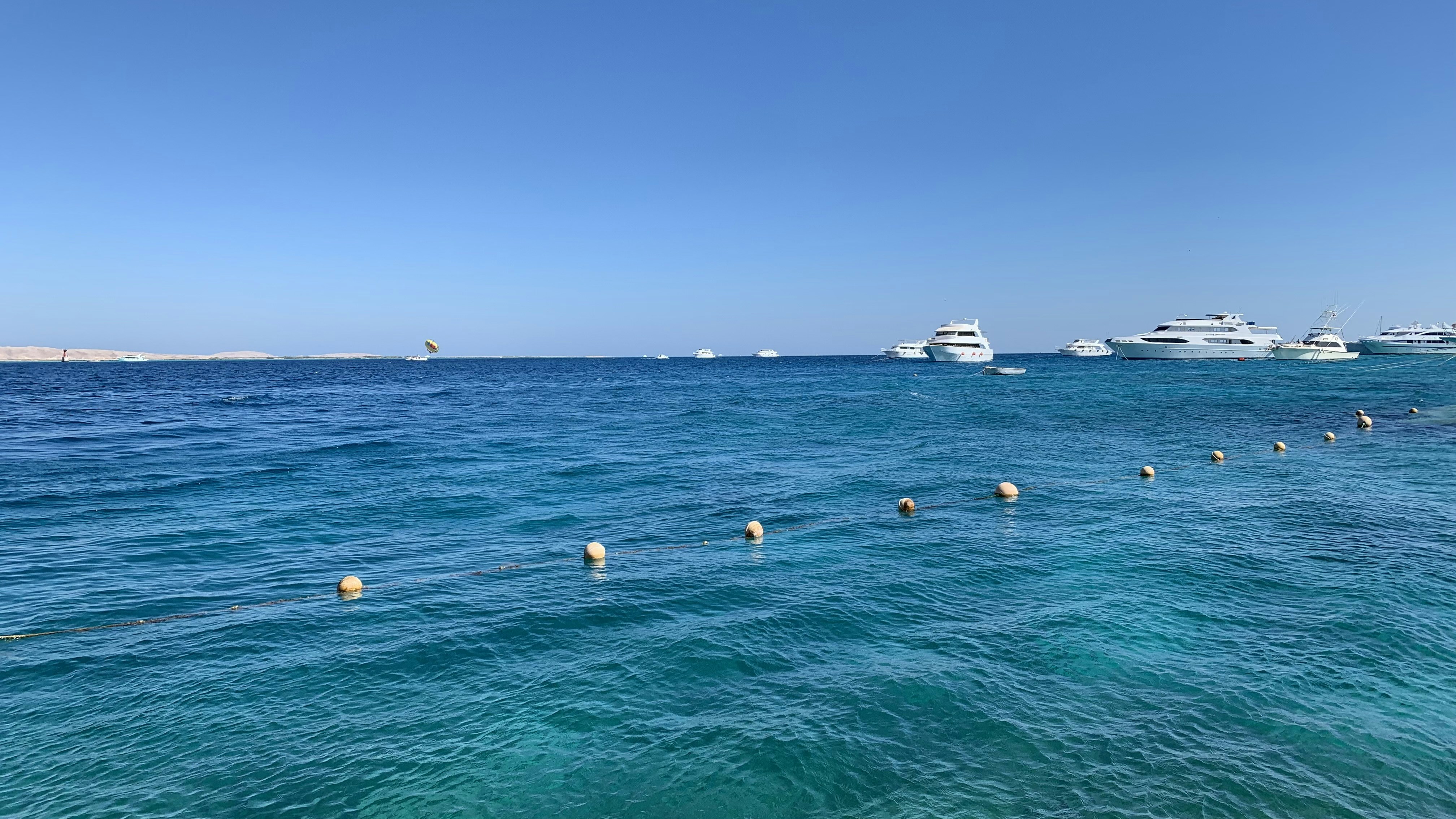 A tranquil seascape featuring a line of yachts anchored in clear blue waters under a bright sky. The scene evokes a sense of relaxation and leisure.