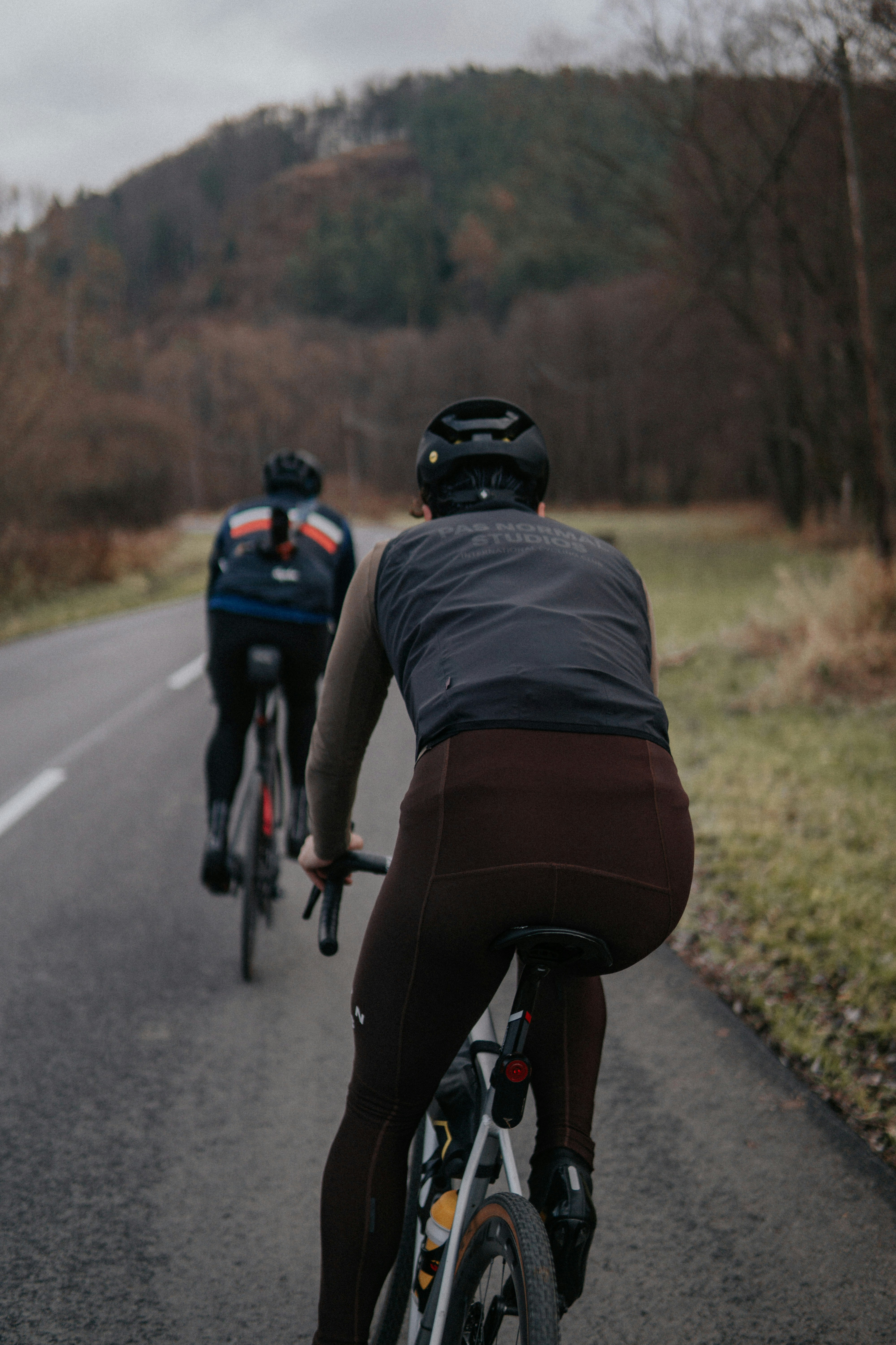 Two cyclists navigate a winding road surrounded by autumn foliage, capturing the essence of outdoor adventure. The scene conveys a sense of movement and tranquility.