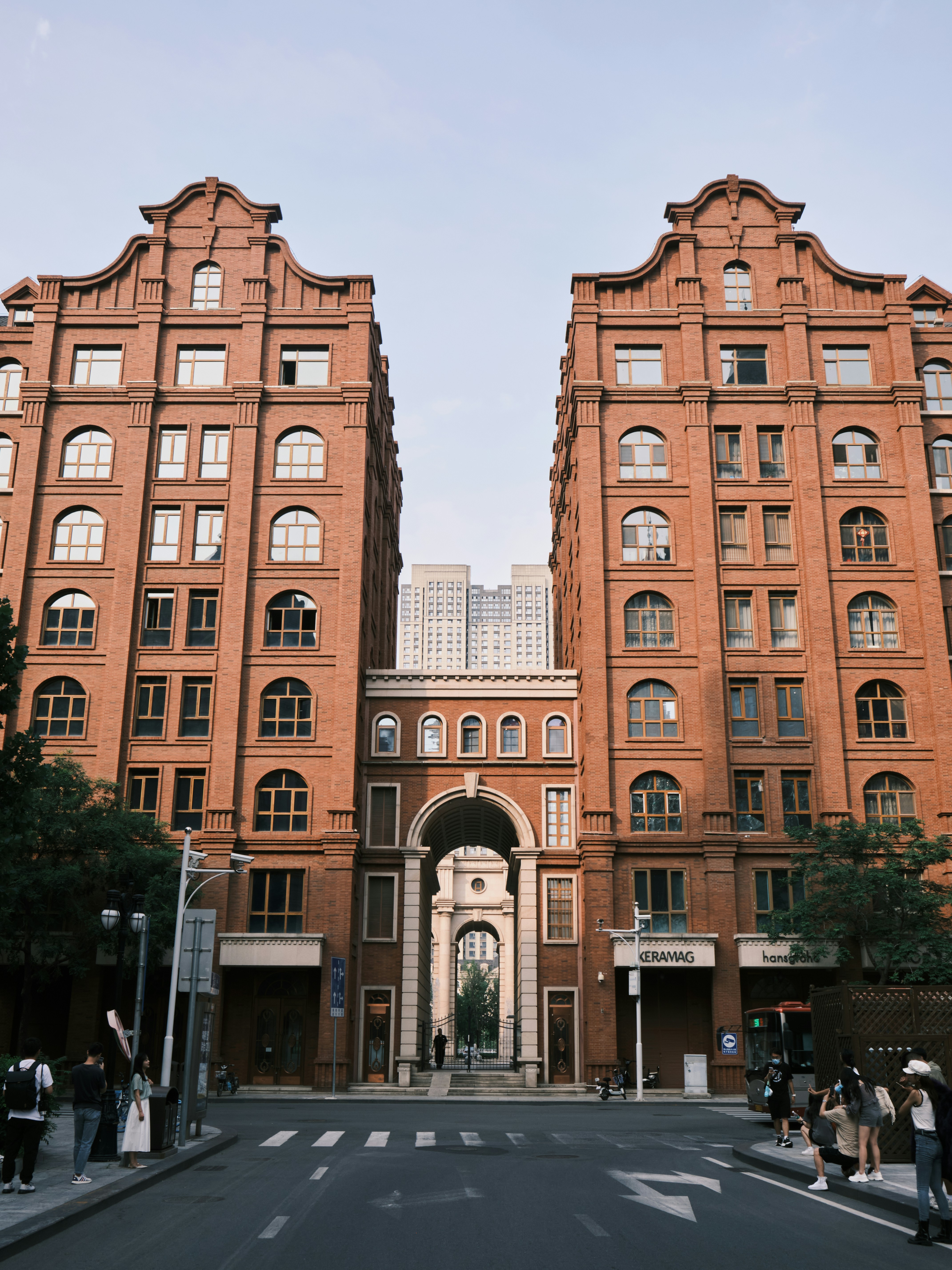 Symmetrical red brick buildings flanking a grand archway, leading to a modern skyline in the background. A blend of historical and contemporary architecture.