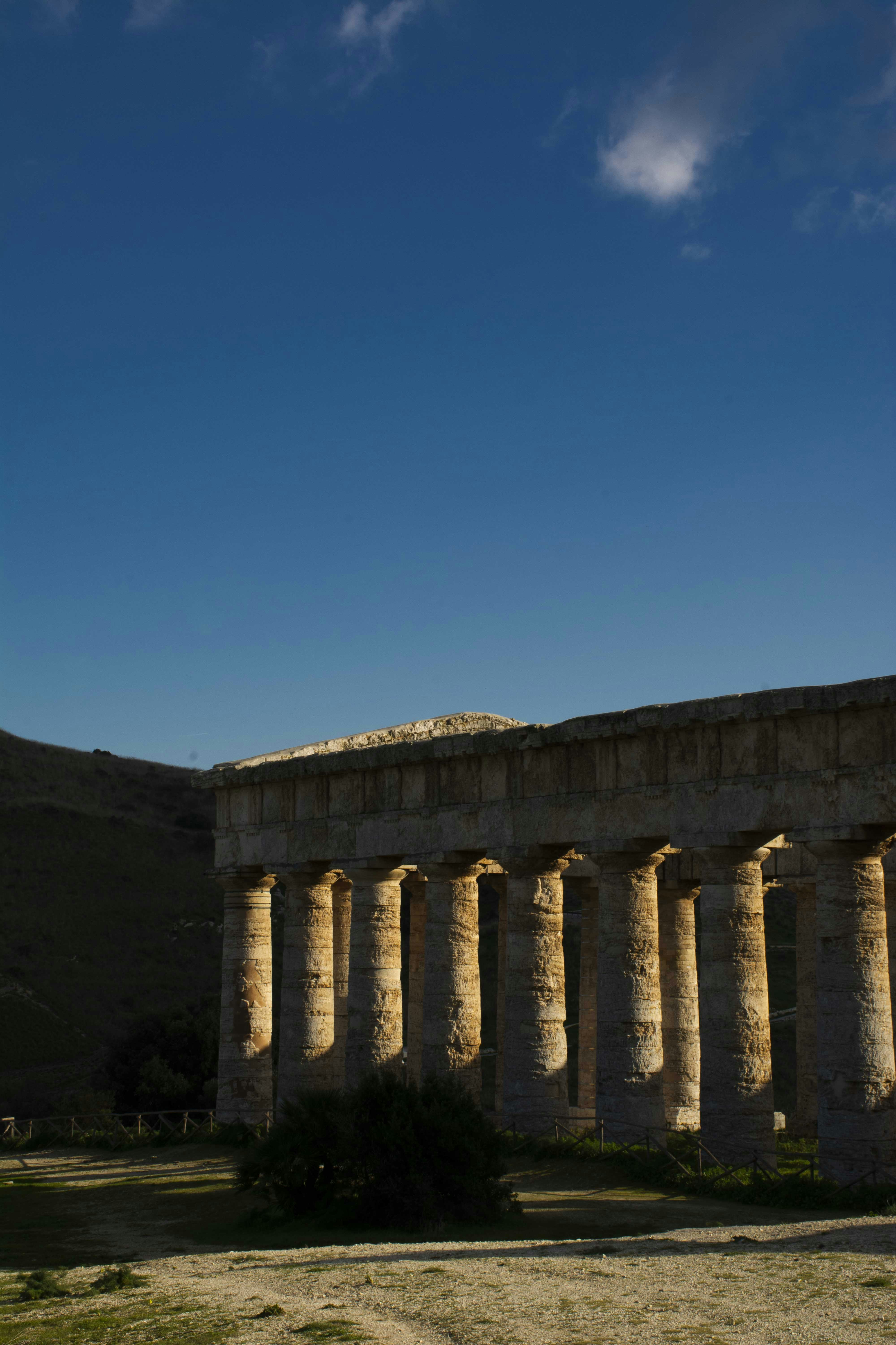 Majestic stone columns of an ancient temple stand against a deep blue sky, partially illuminated by sunlight.