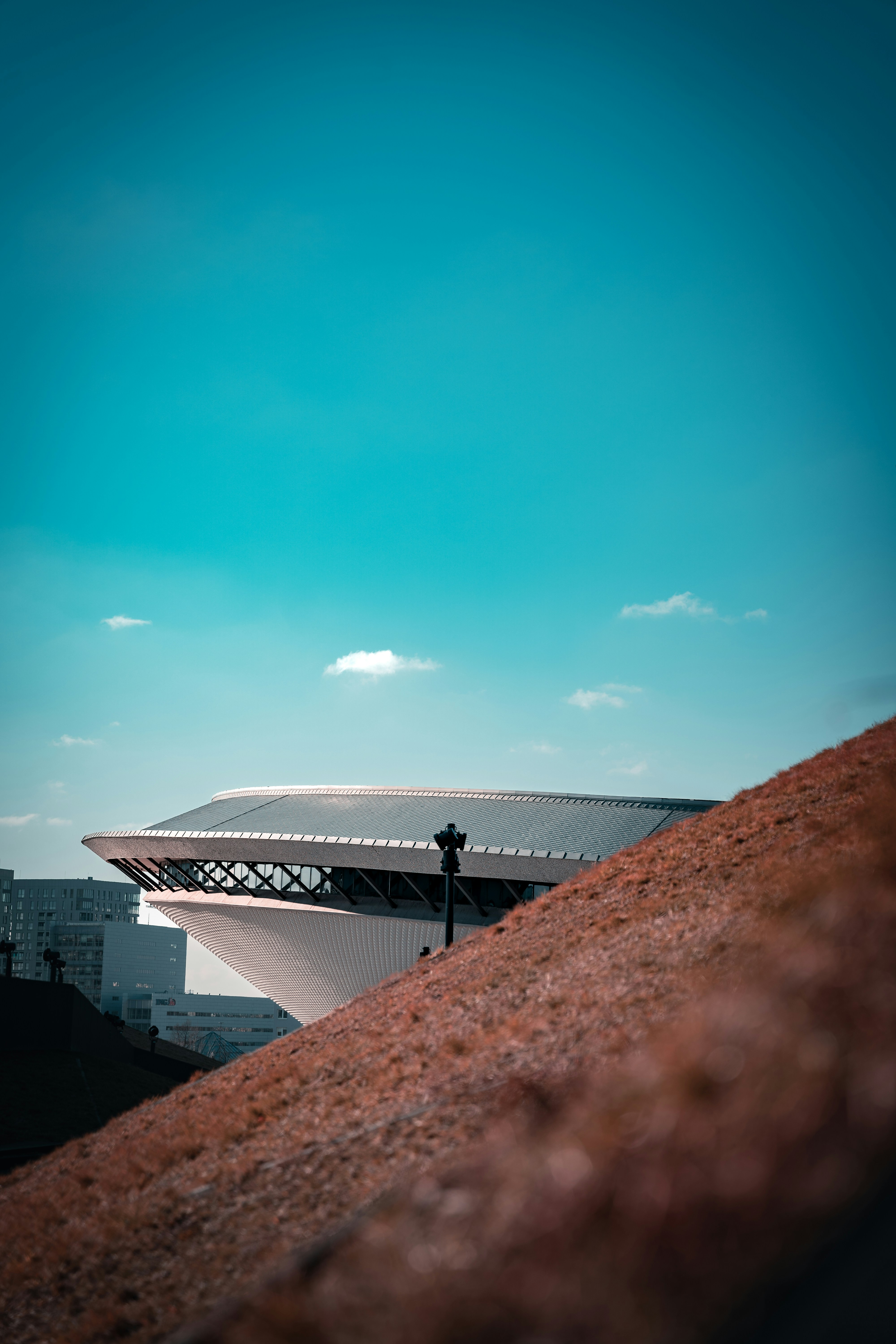 A modern architectural structure peeks over a textured hillside under a clear blue sky, showcasing innovative design and urban landscape integration.