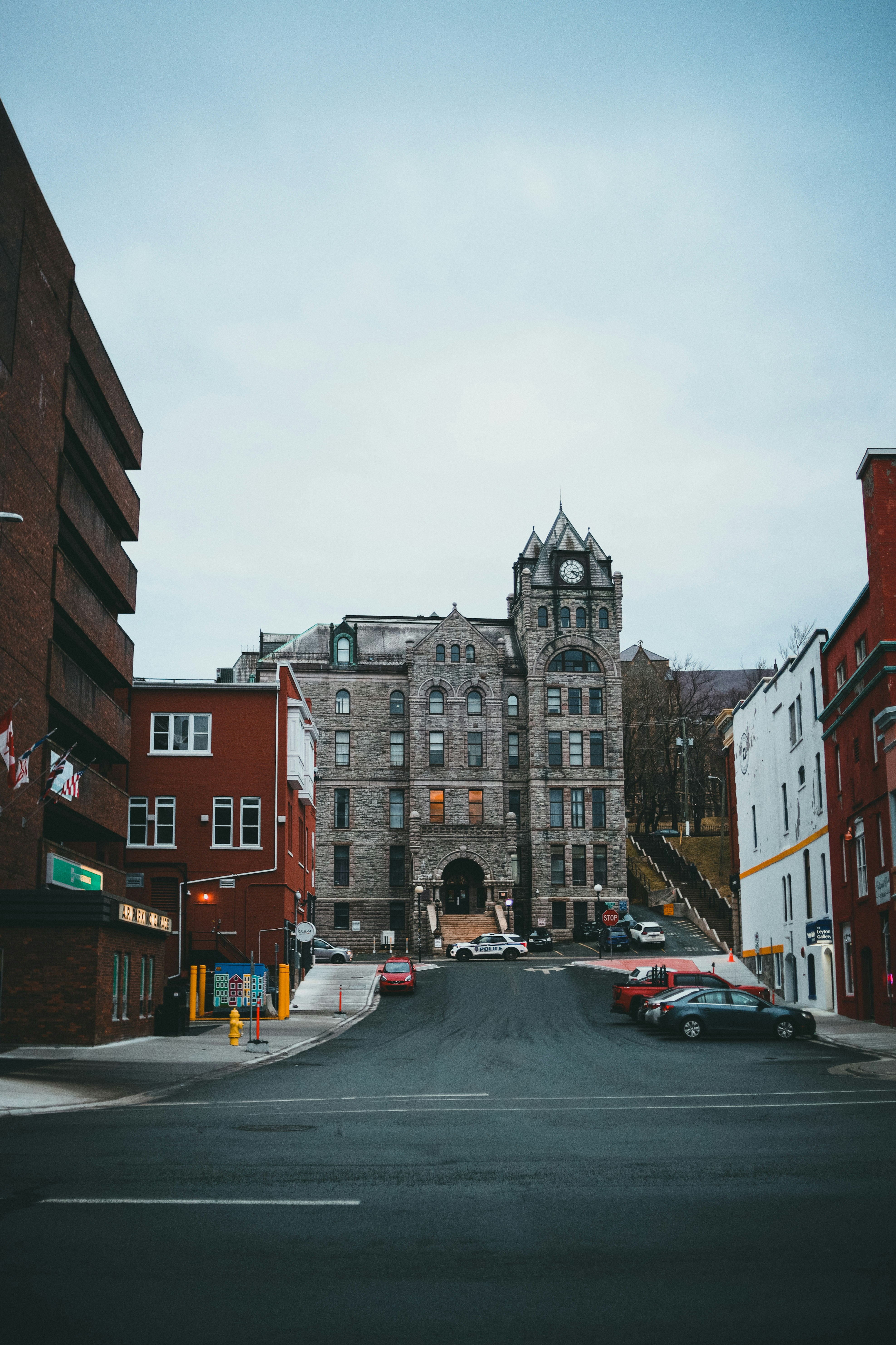 Historic stone building rising prominently at the end of a city street, flanked by modern structures. The scene captures a blend of architectural styles and urban life.