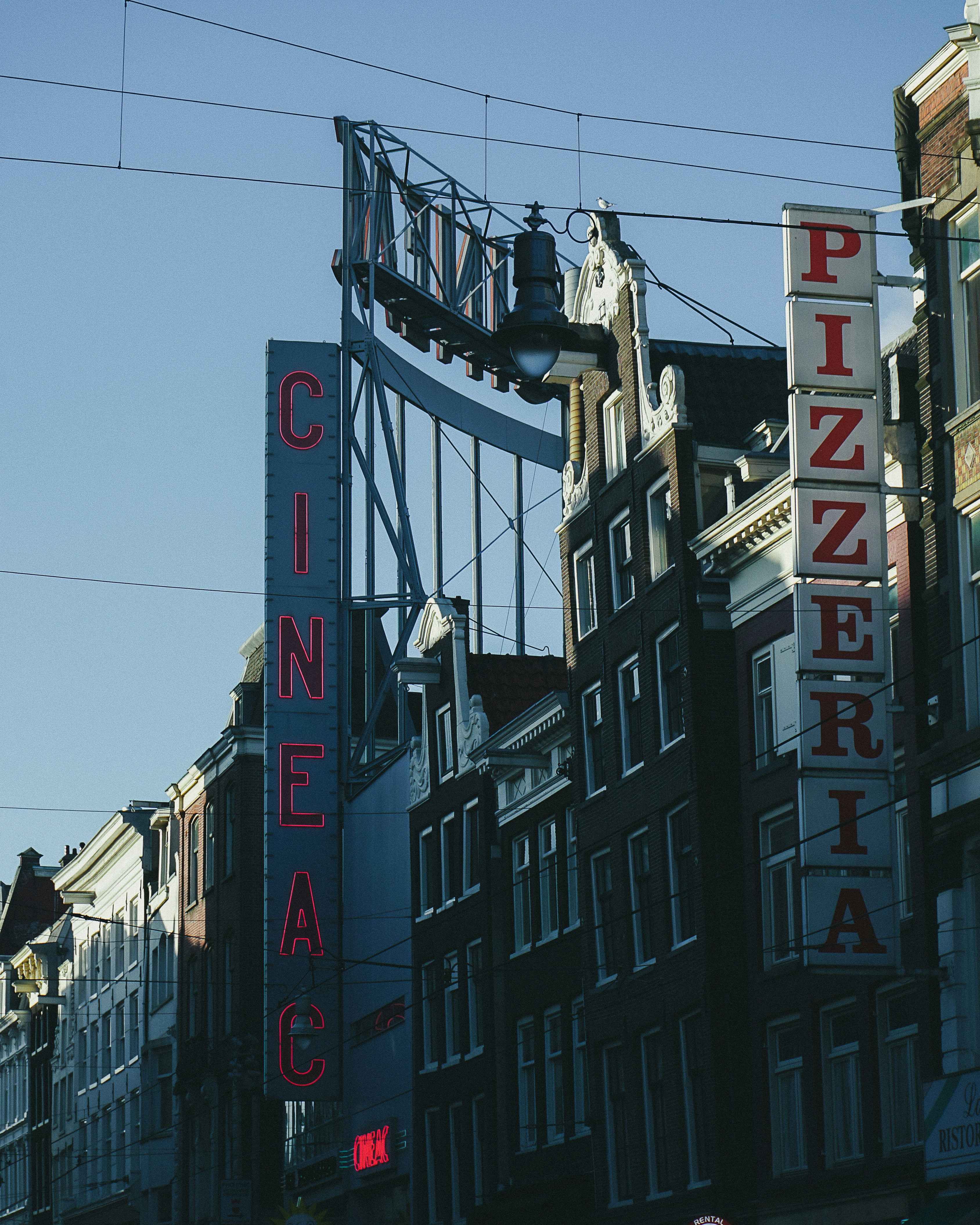 Neon Between Bricks: Cinema and Pizzeria Signage Framed by Steel