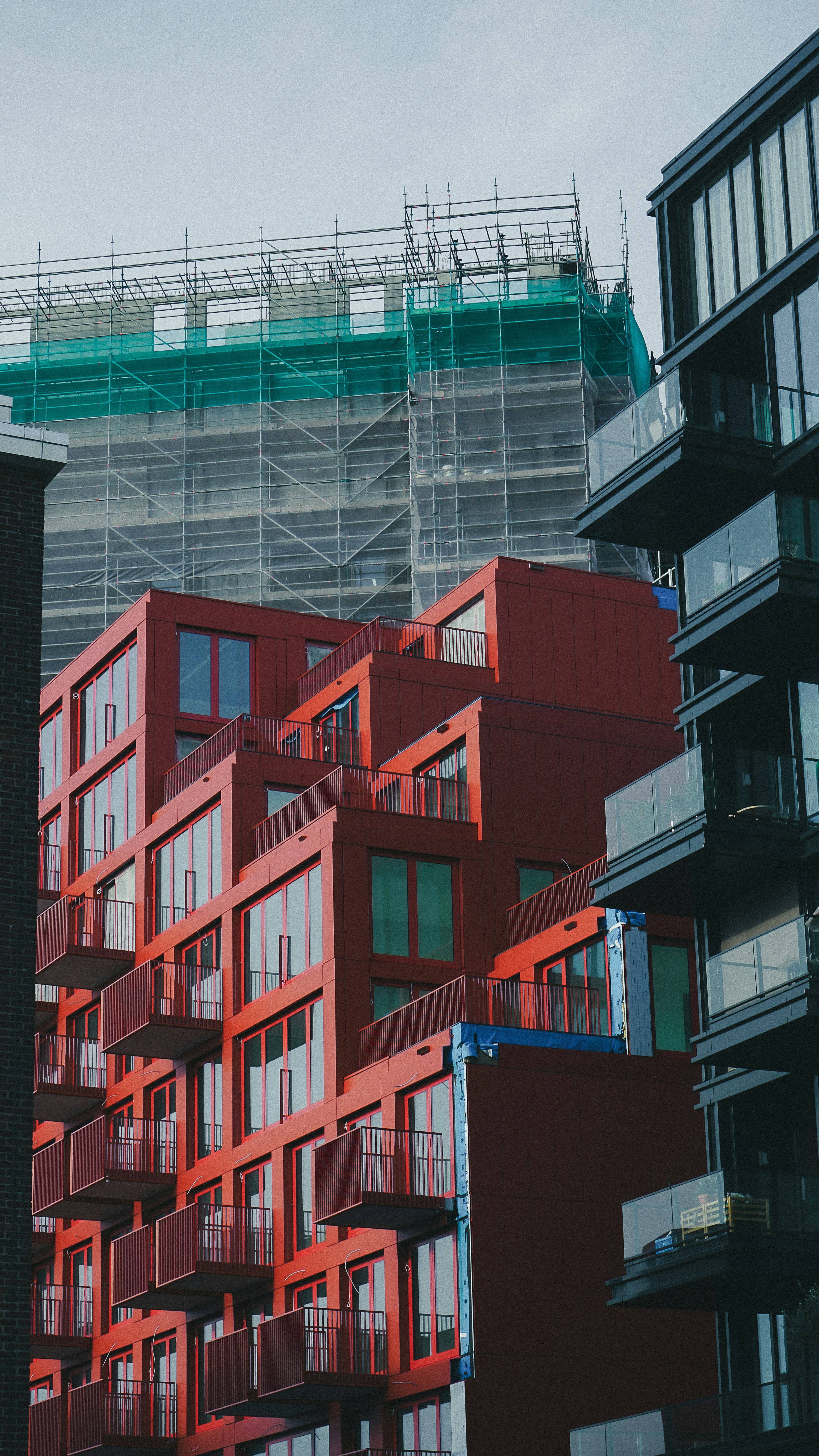 Vibrant red apartment complex juxtaposed against a construction site, showcasing modern architectural design elements. The image captures the contrast between completed and ongoing developments.