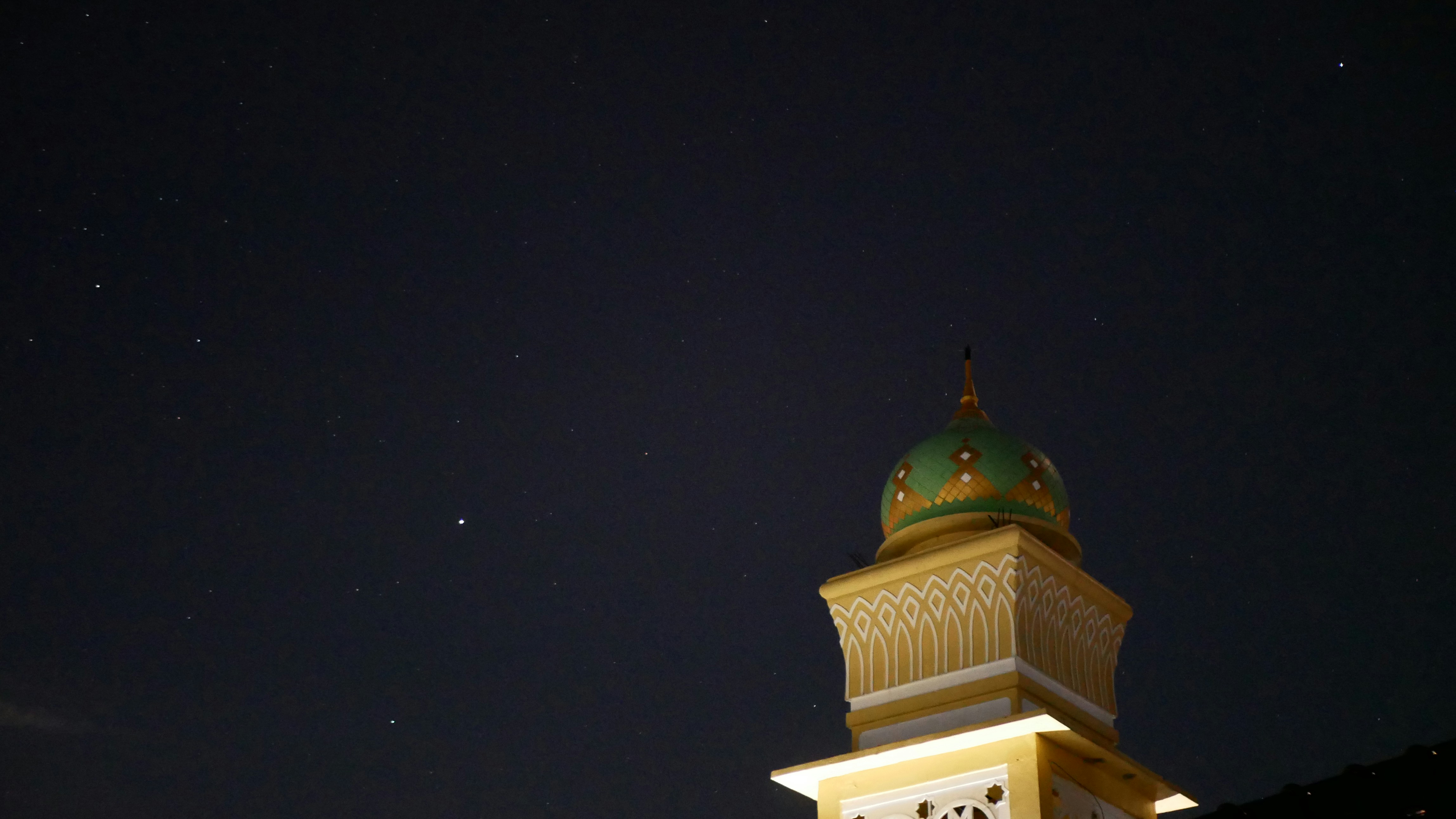 A beautifully illuminated minaret against a starry night sky, showcasing intricate architectural details and a vibrant dome. 