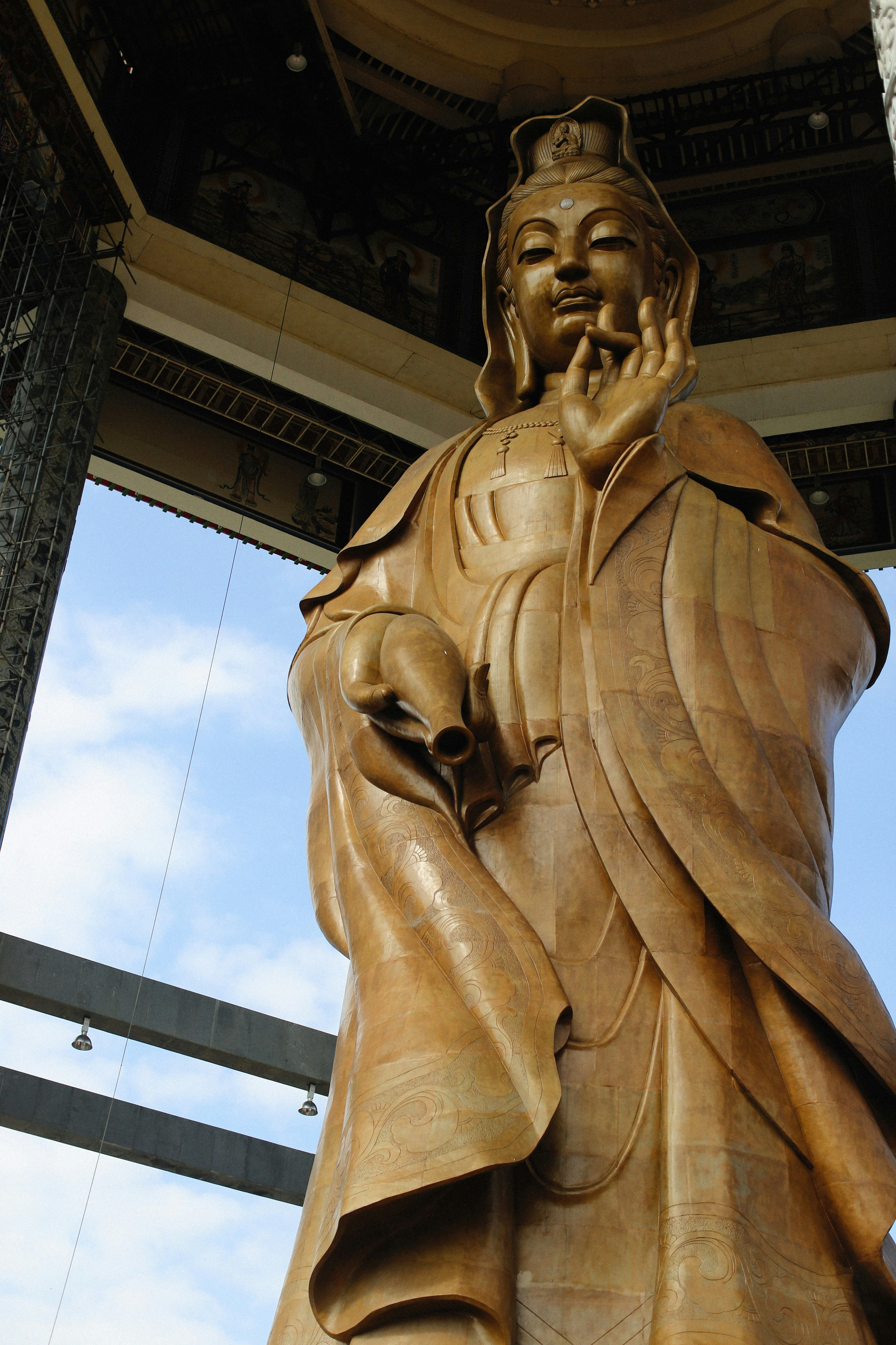 Majestic wooden statue of a serene figure, embodying peace and wisdom, set against a backdrop of an open sky.