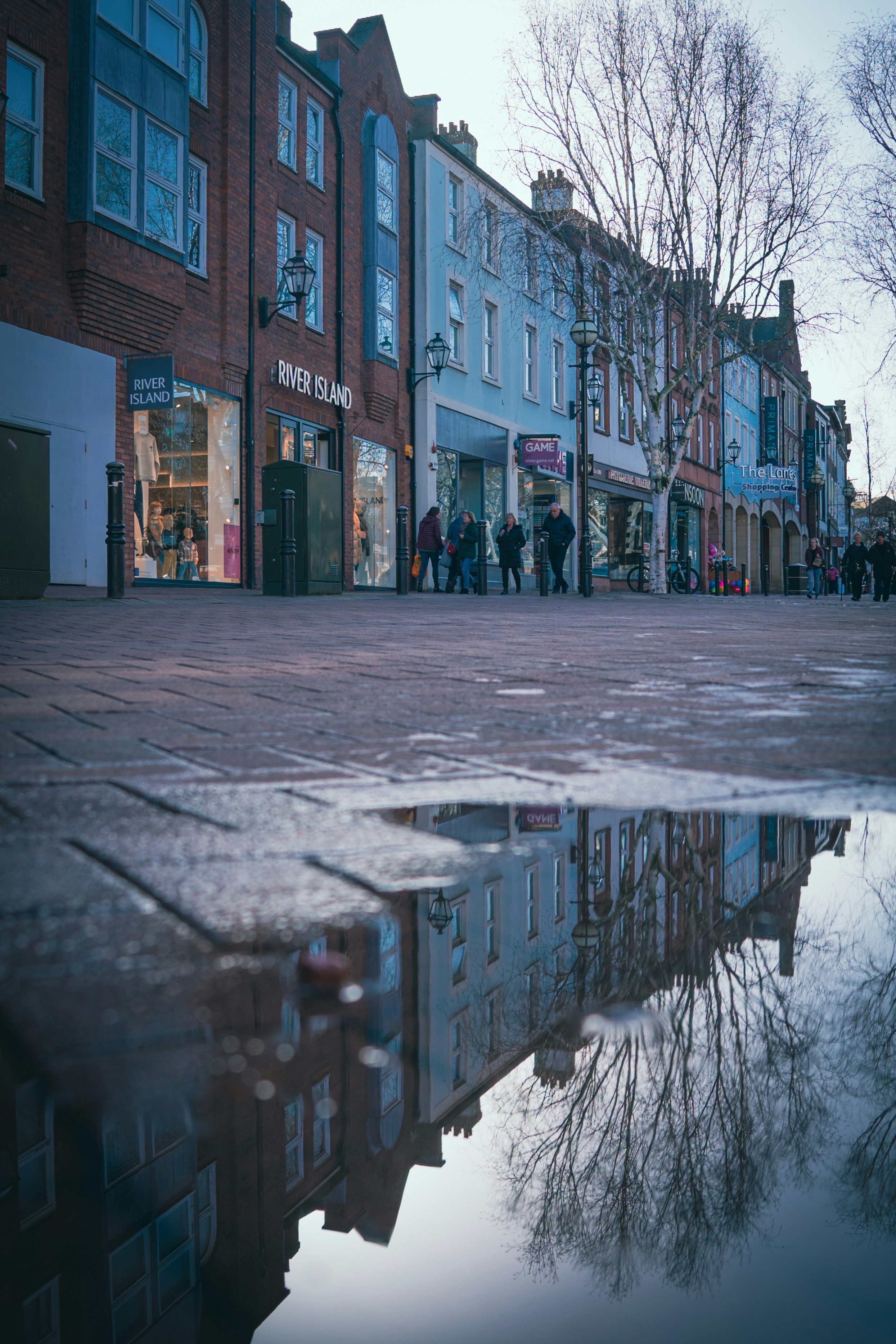 Blue Hour Boulevard: Pedestrians and Reflections Along a Row of Shops