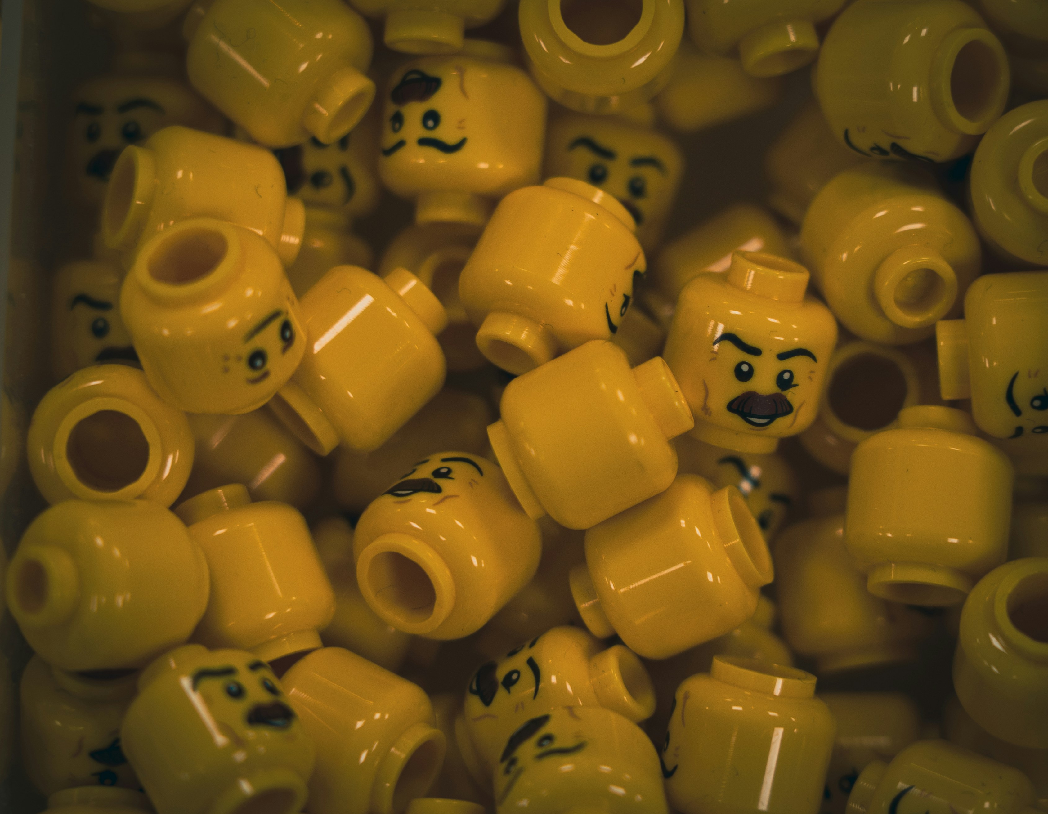A collection of yellow Lego heads with various facial expressions scattered in a box.