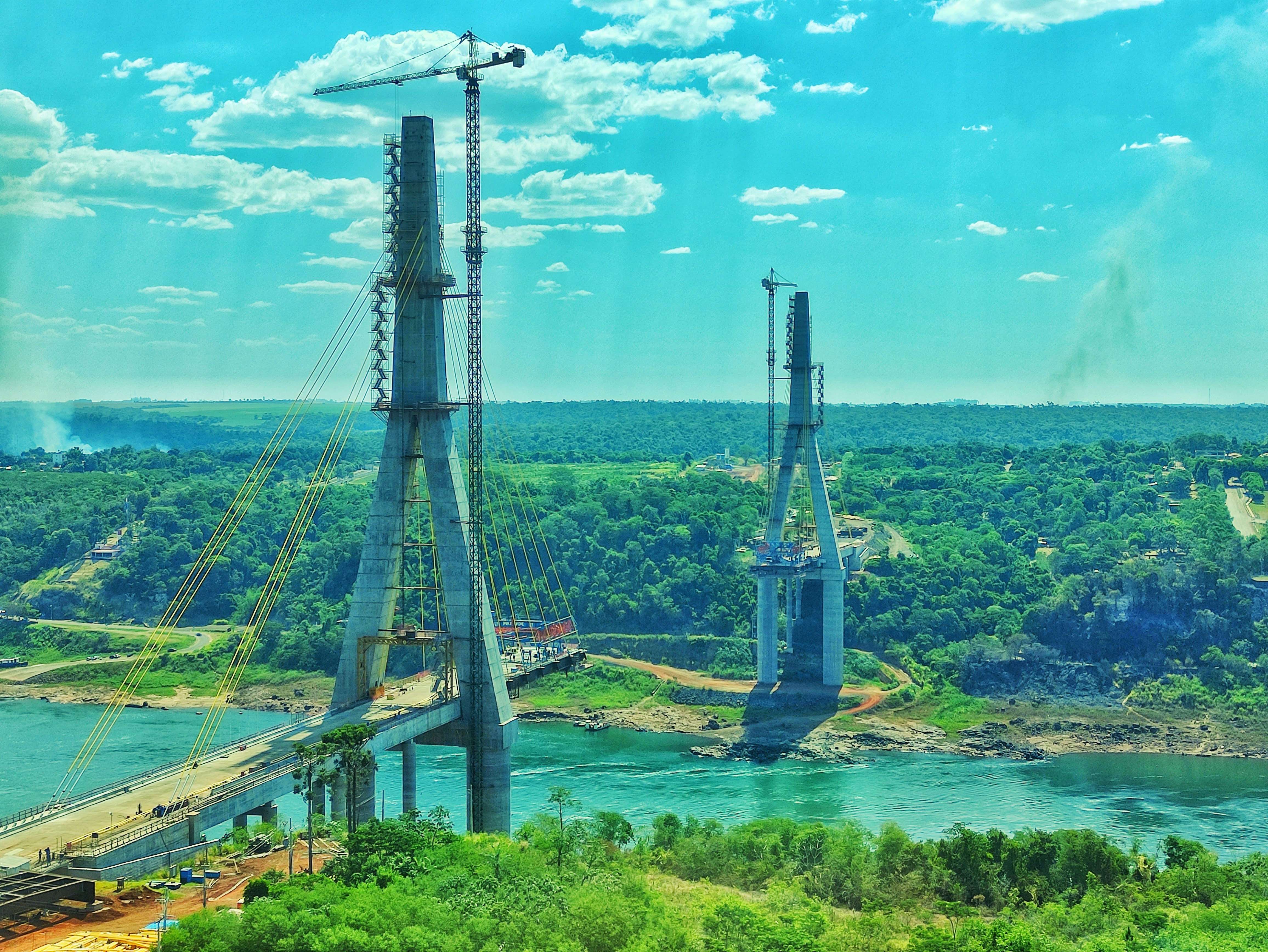 Suspended bridge towers stand tall against a vibrant sky, showcasing engineering prowess amidst lush greenery and flowing water.