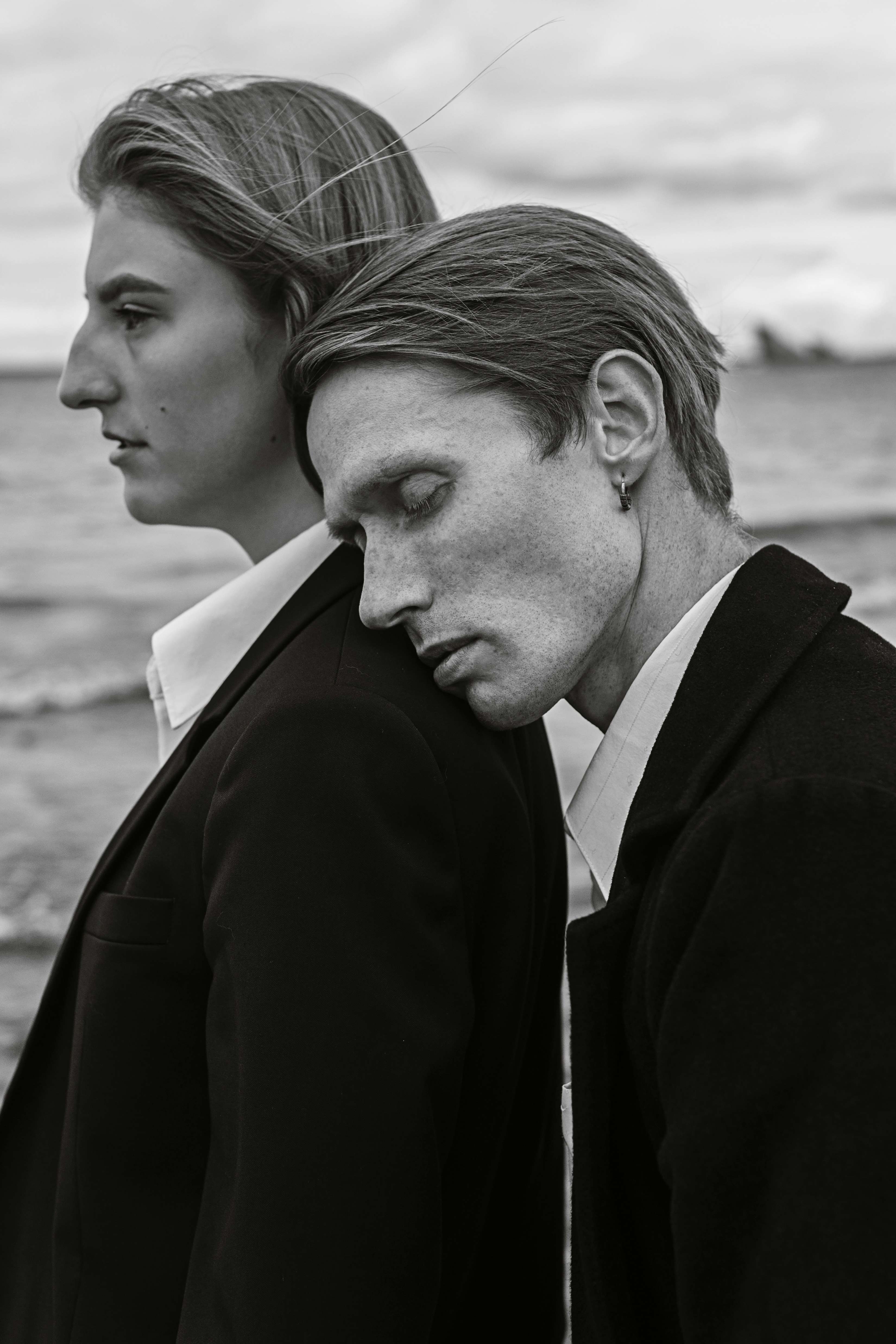 Seaside Noir: Two tailored silhouettes lean on each other at the edge of the sea.