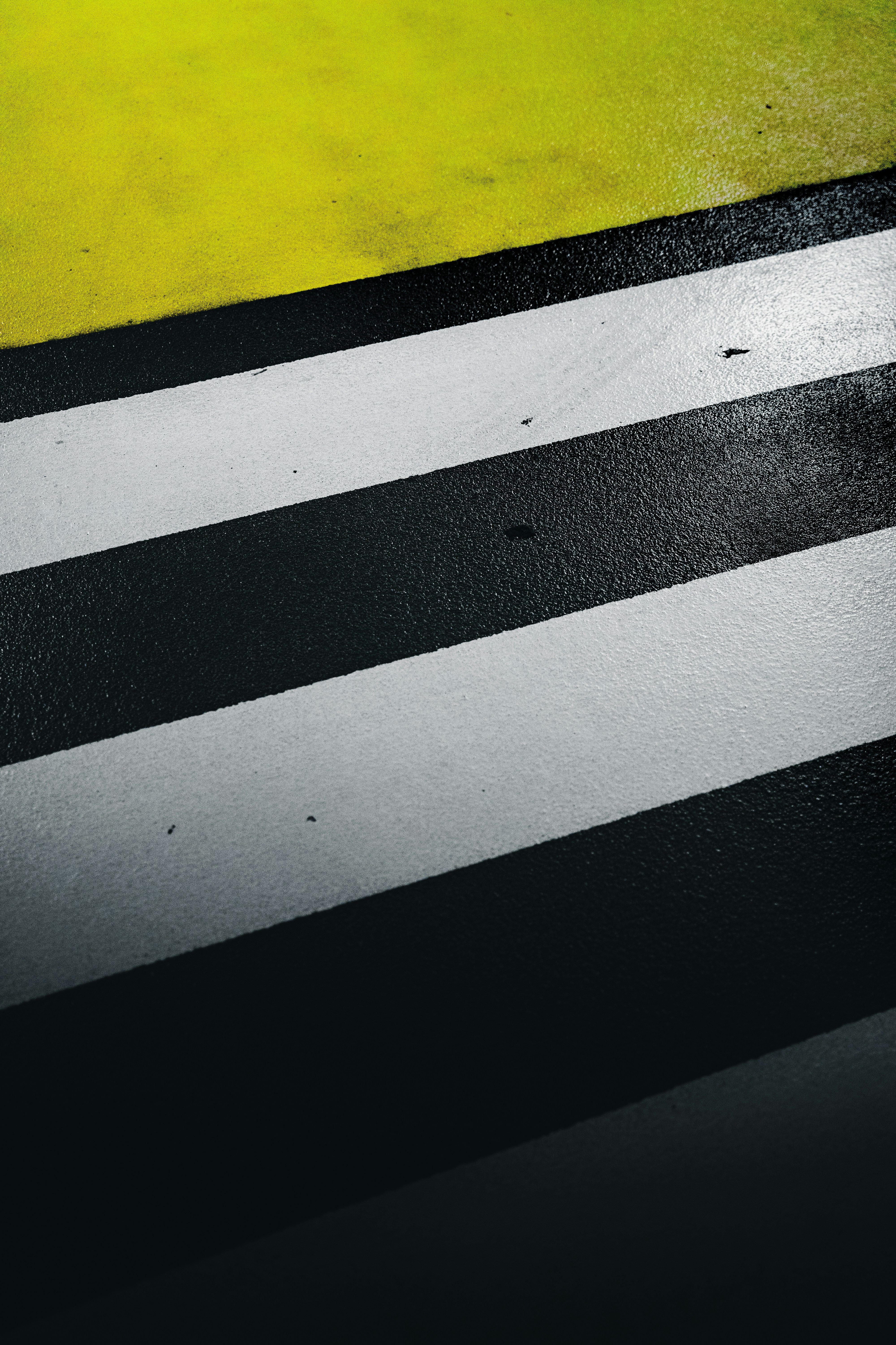 Diagonal stripes of black and white paint intersect with a vibrant yellow surface, creating a striking abstract composition.