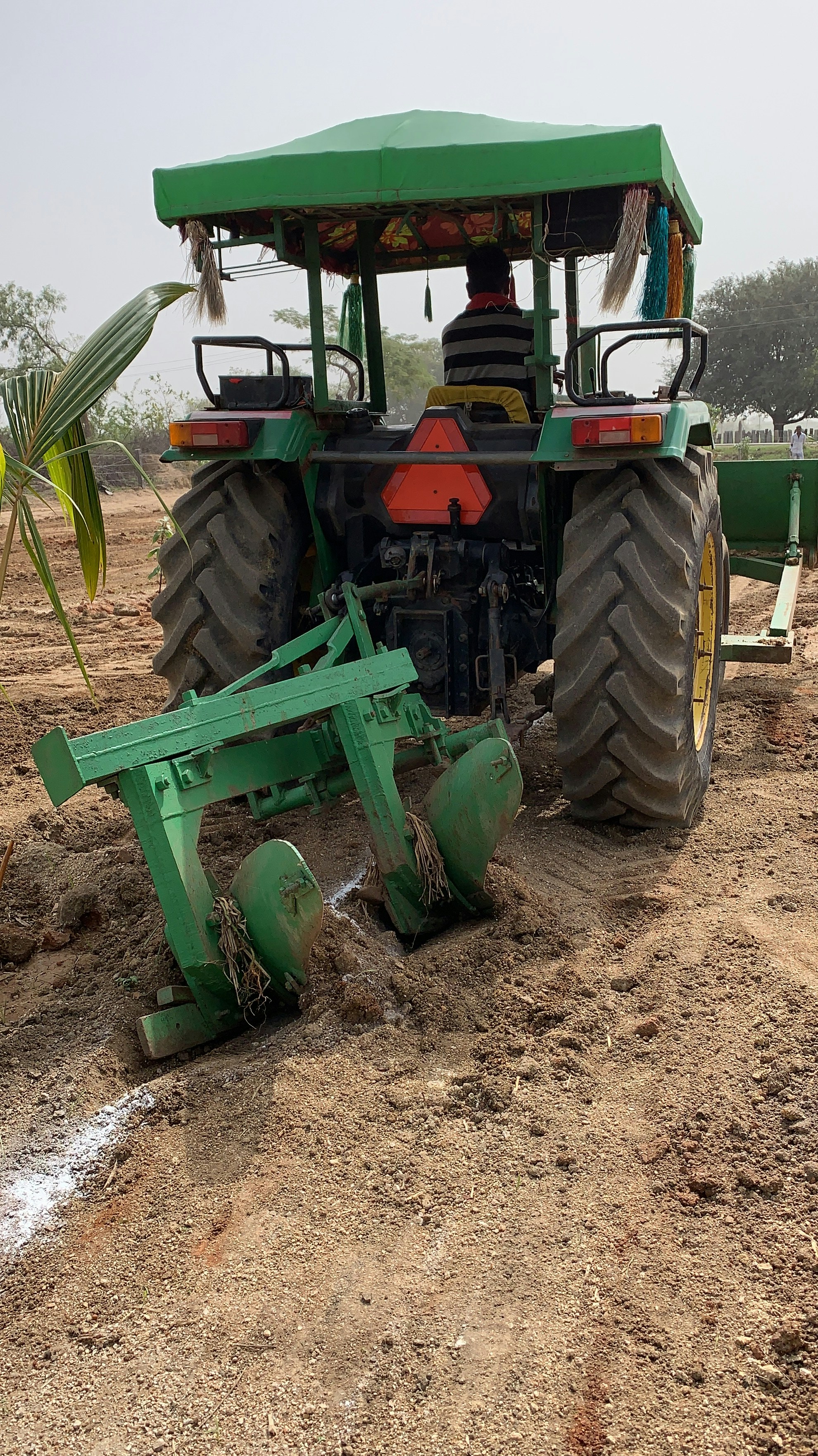 A green tractor equipped with agricultural tools plows through sandy soil, showcasing modern farming techniques in action.