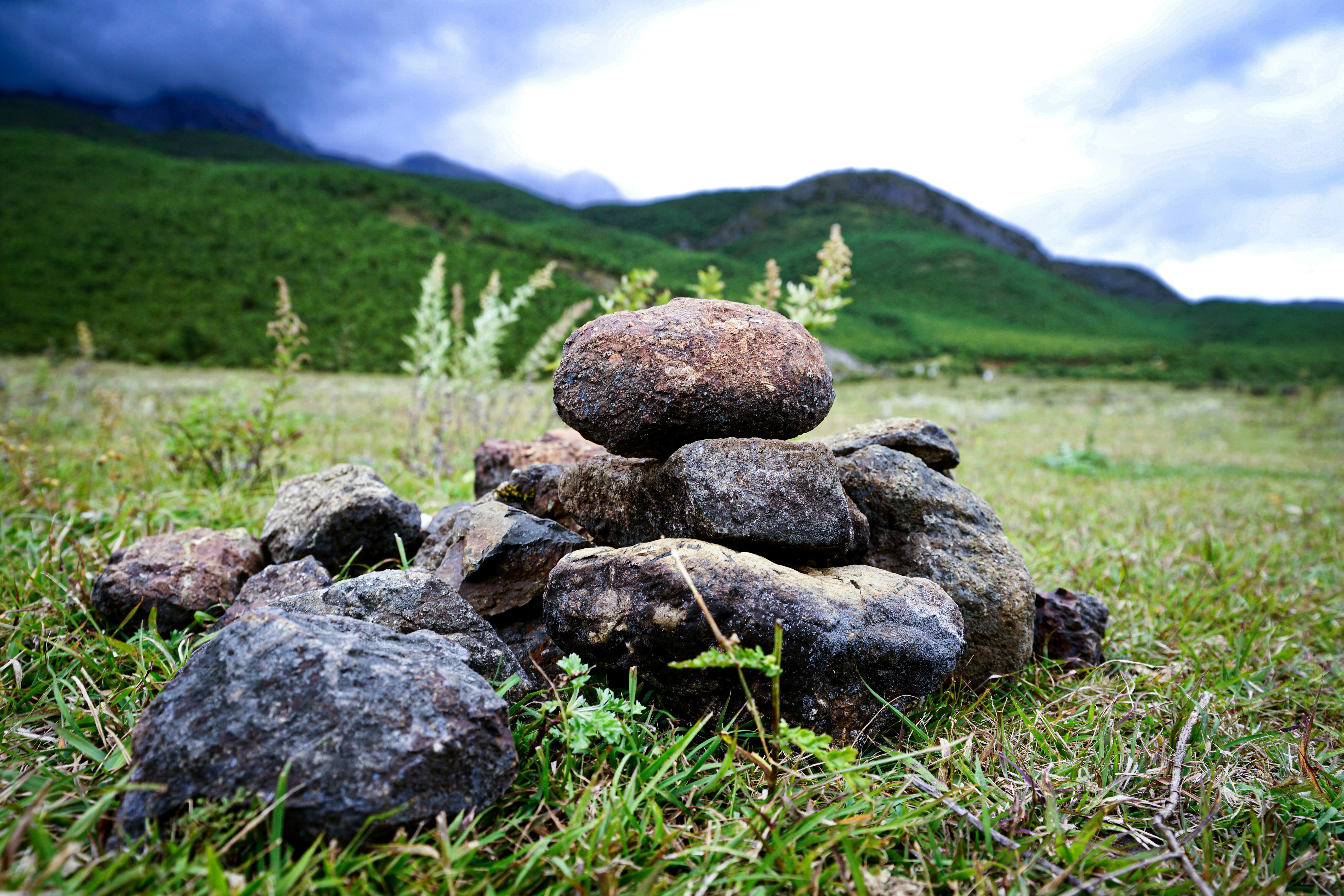 A carefully stacked arrangement of stones in a grassy field, surrounded by lush greenery and distant mountains under a moody sky.