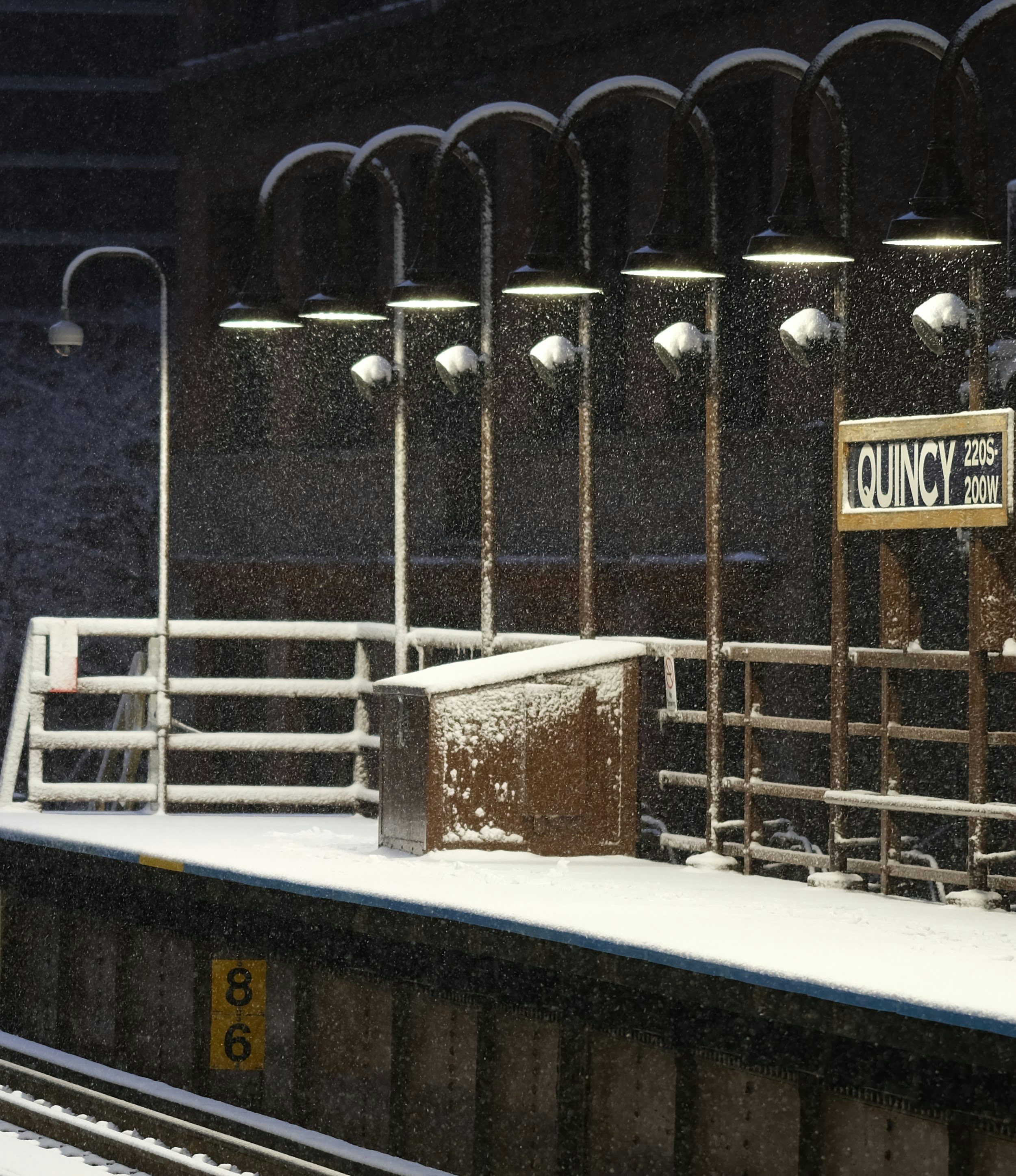 Snow blankets the Quincy train station platform, illuminated by vintage street lamps, creating a serene winter scene.