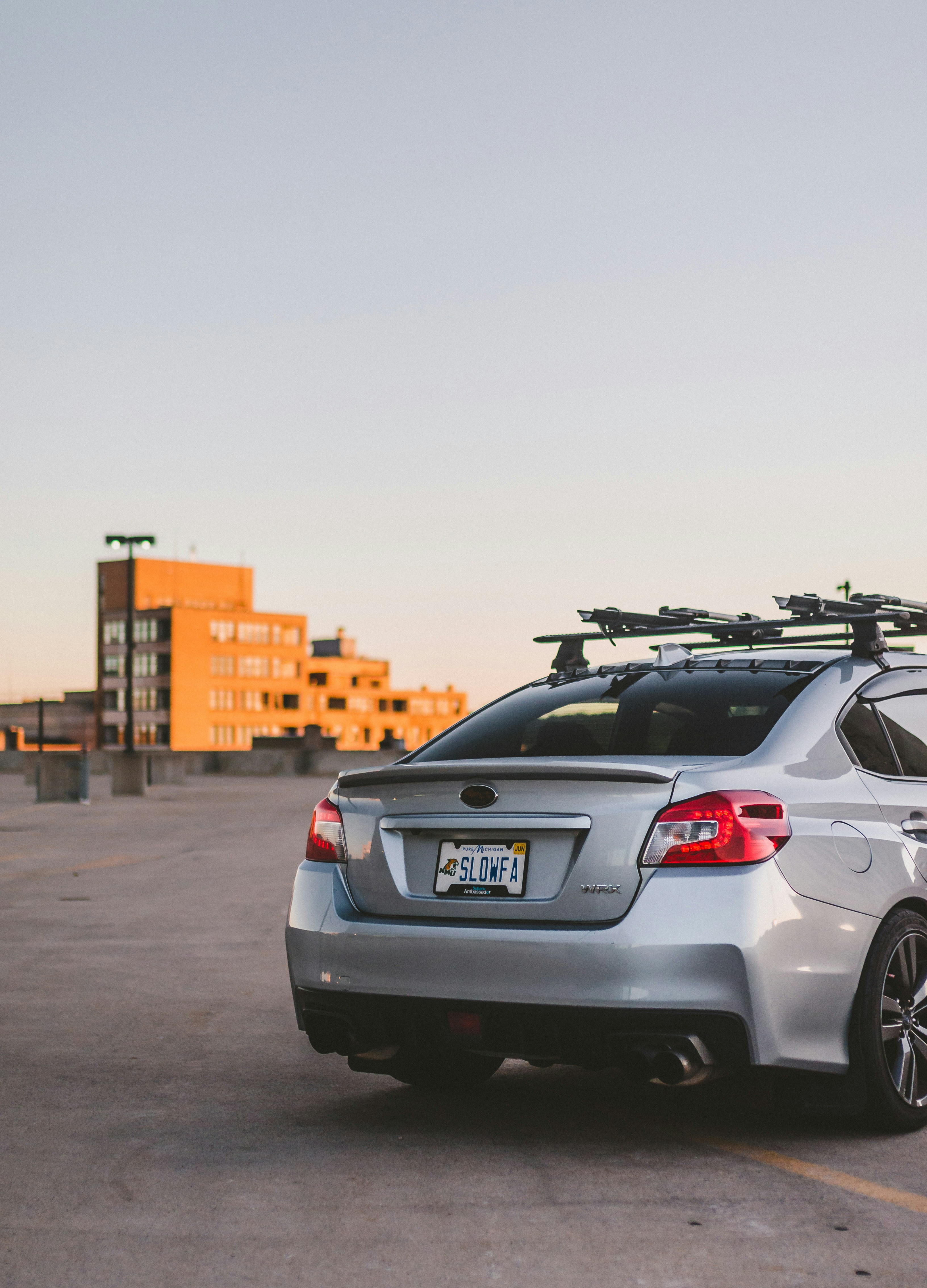 Rear-Loaded Road Trip: A Silver Sedan with Roof Racks Anchoring the Urban Rooftop