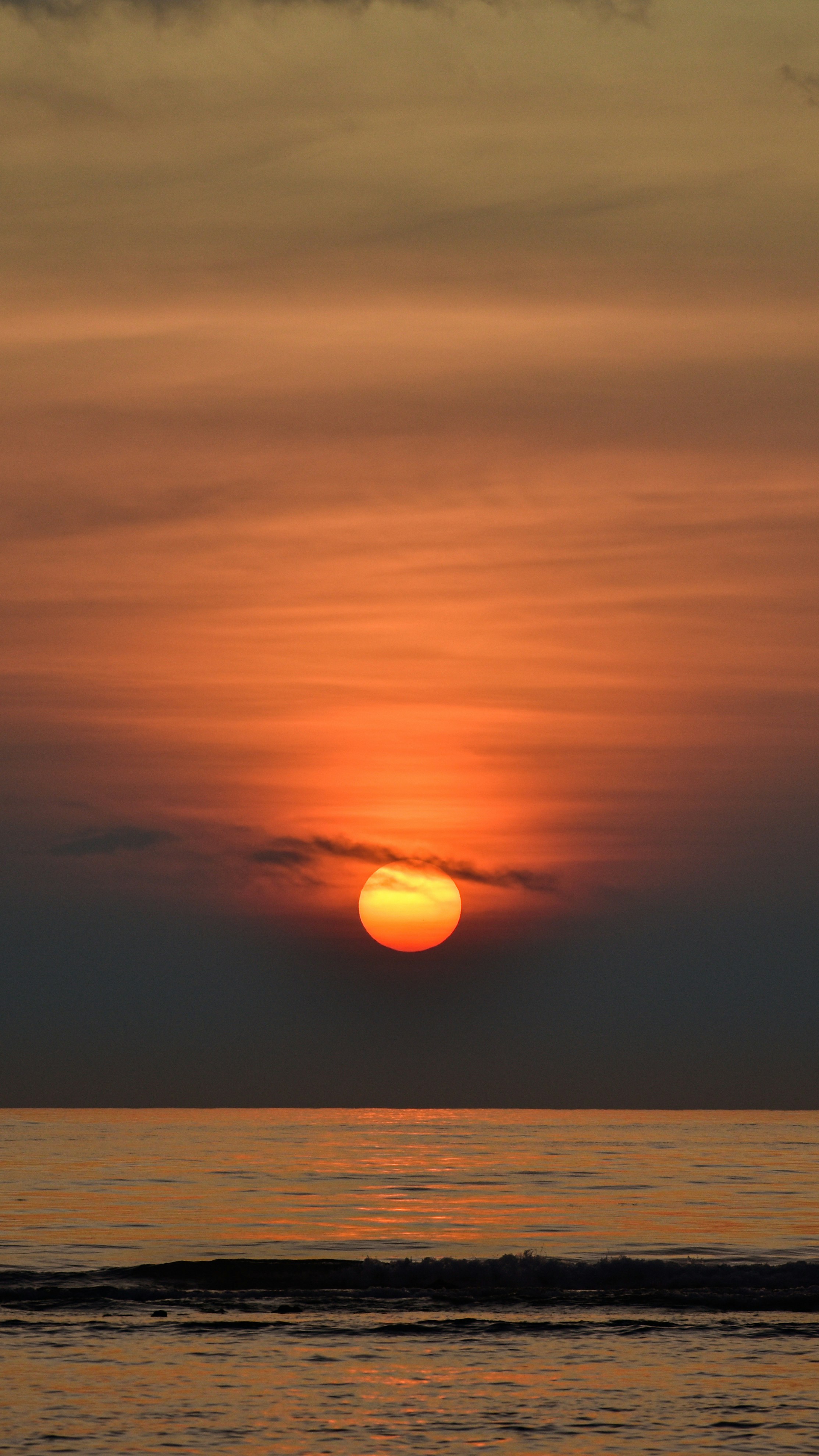 Golden sun dipping below the horizon, casting warm hues across the tranquil sea surface.