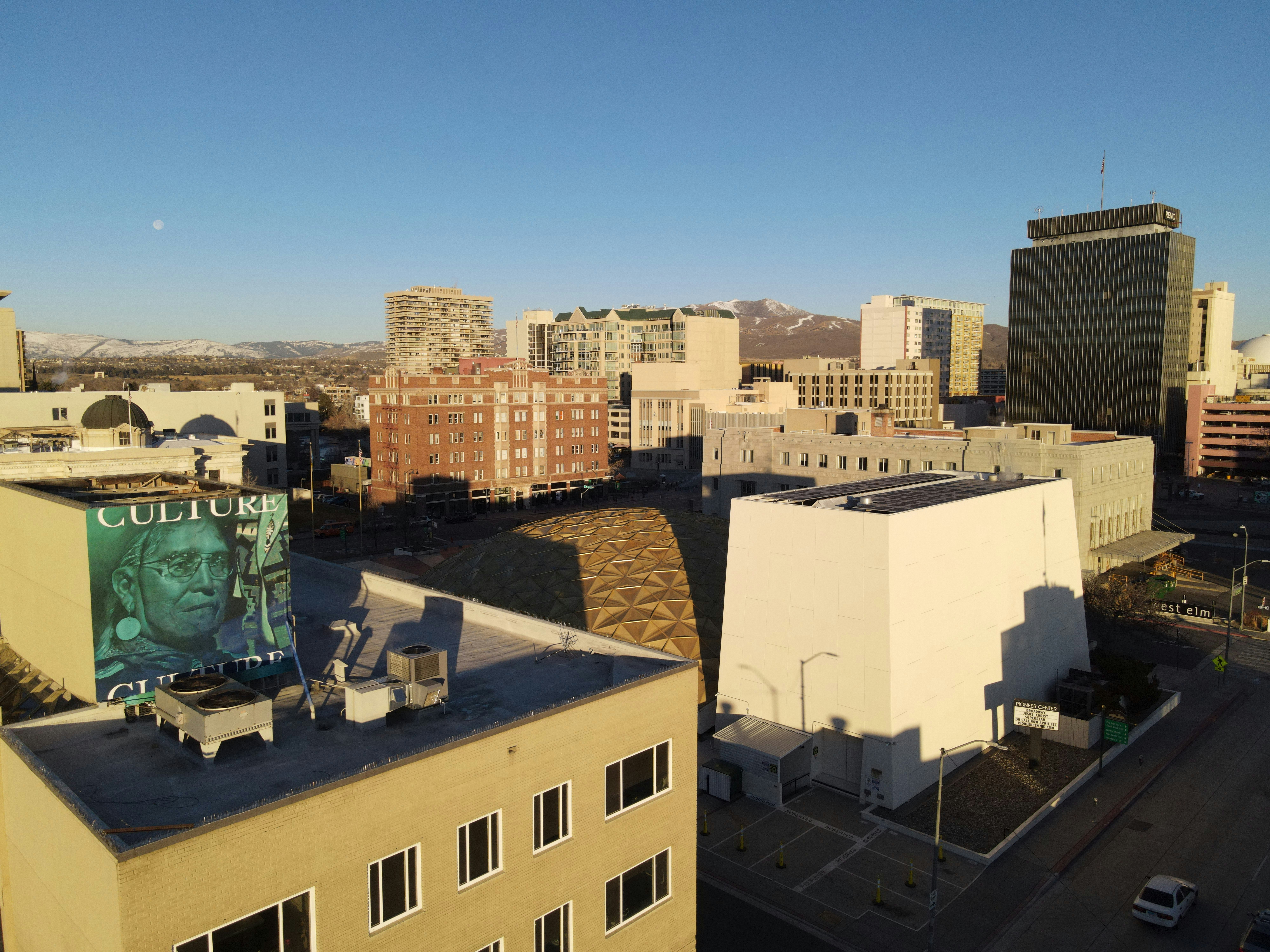 Vibrant mural depicting a cultural figure on a building in a bustling cityscape, with snow-capped mountains in the background.