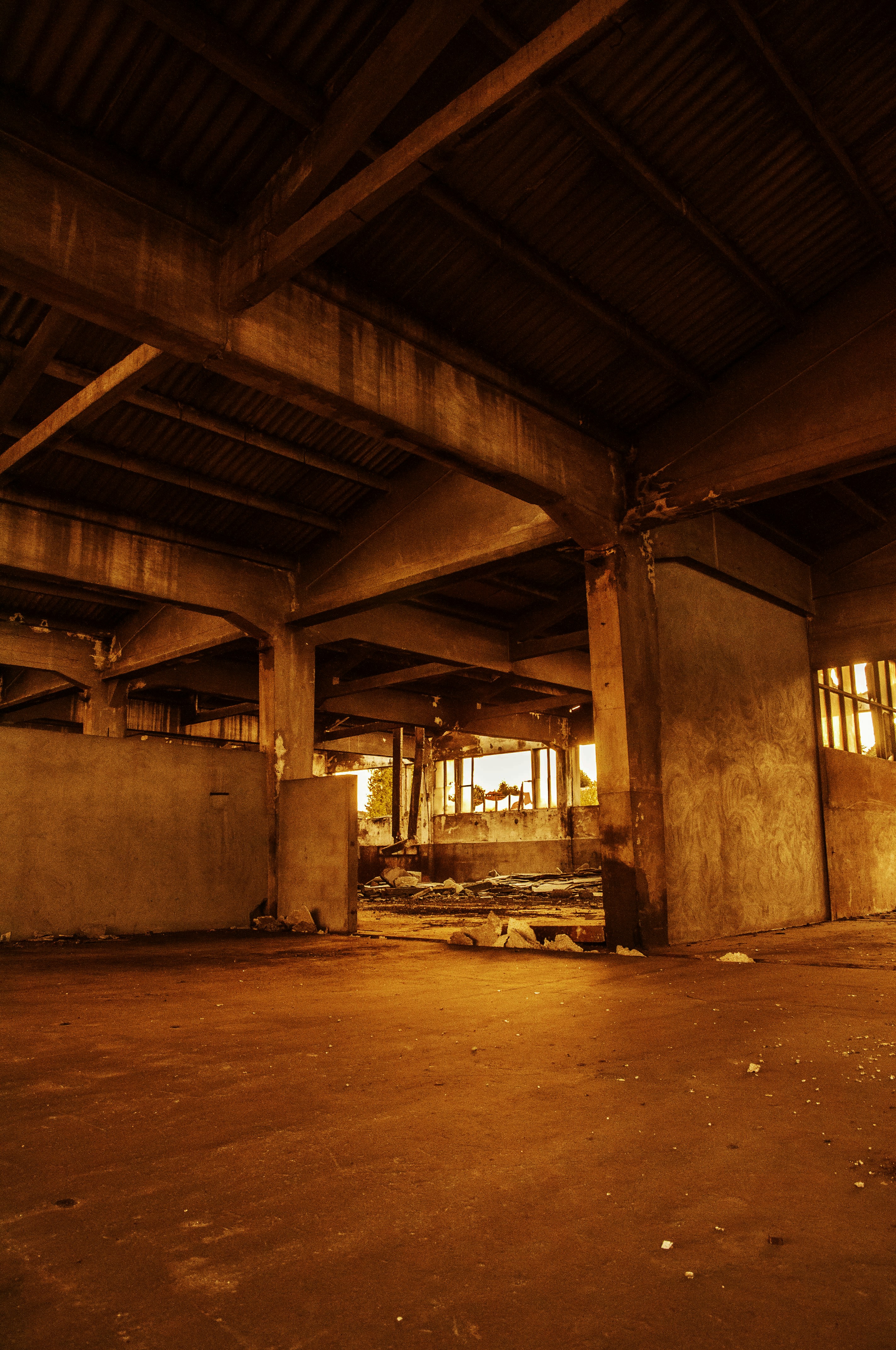 Abandoned industrial interior showcasing weathered concrete structures and scattered debris, illuminated by warm, golden light.