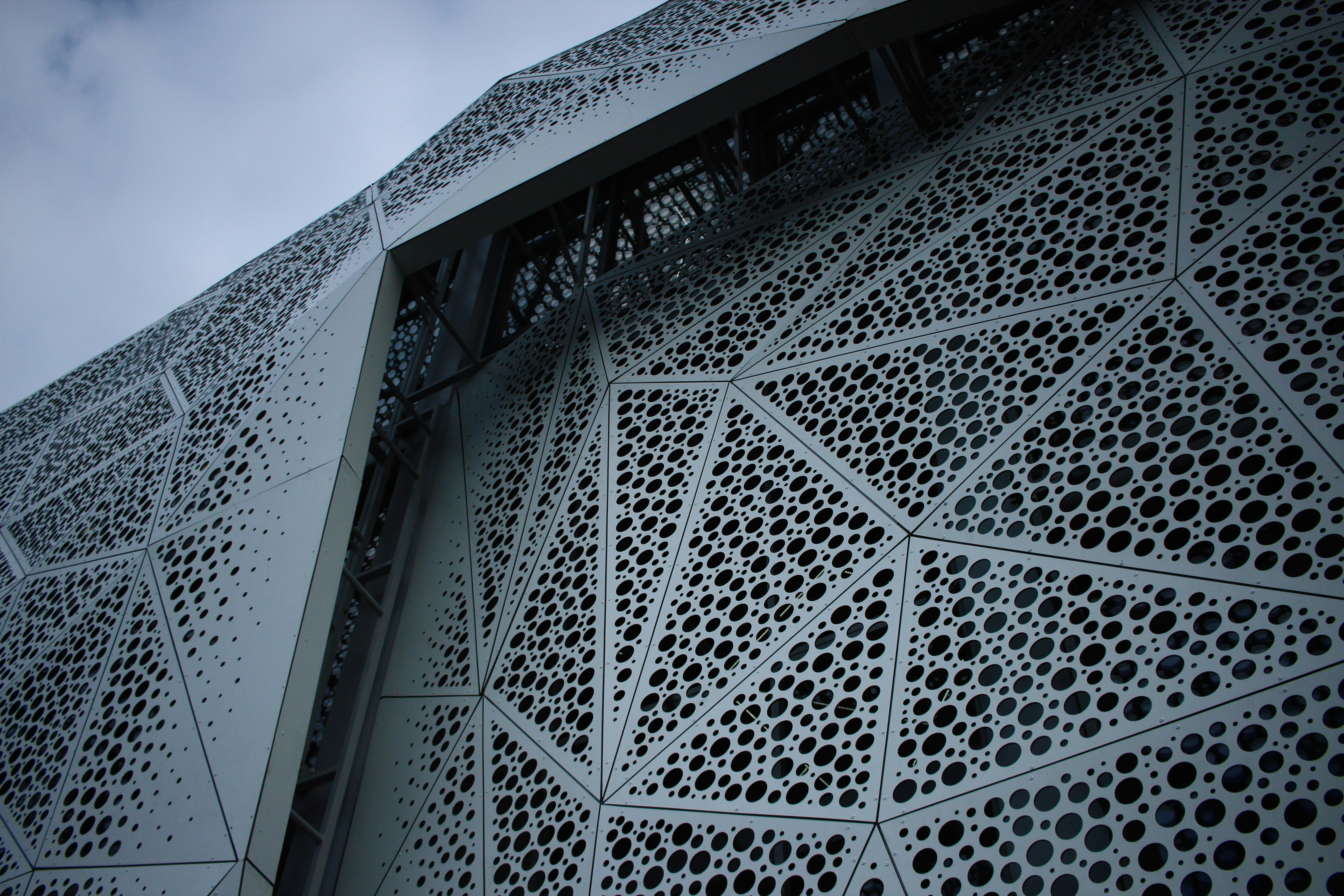 Intricate perforated metal facade showcasing a modern architectural design with a dynamic interplay of light and shadow.