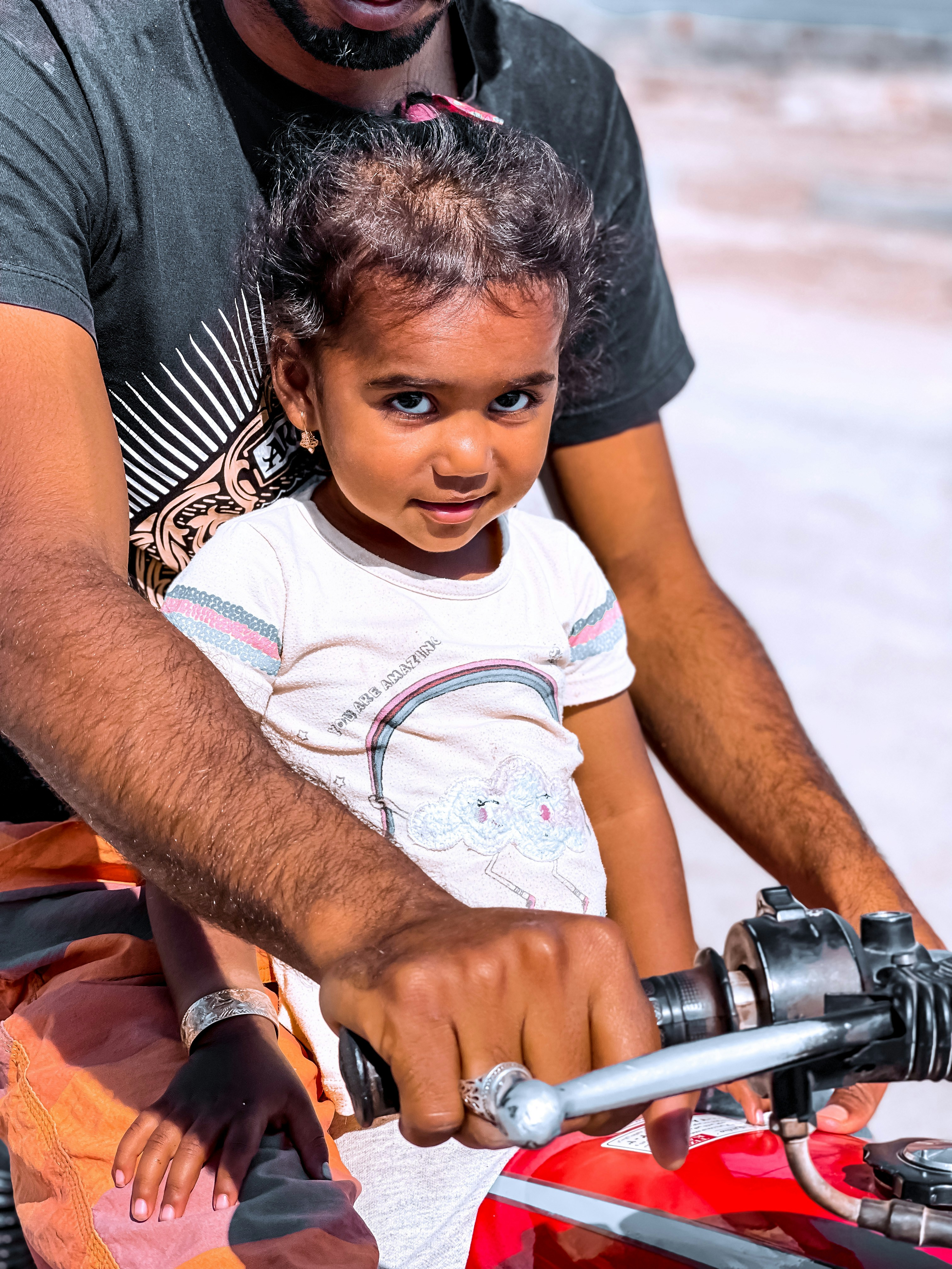 Little Co-Pilot: The Girl Seated Between Hands on a Red Motorcycle