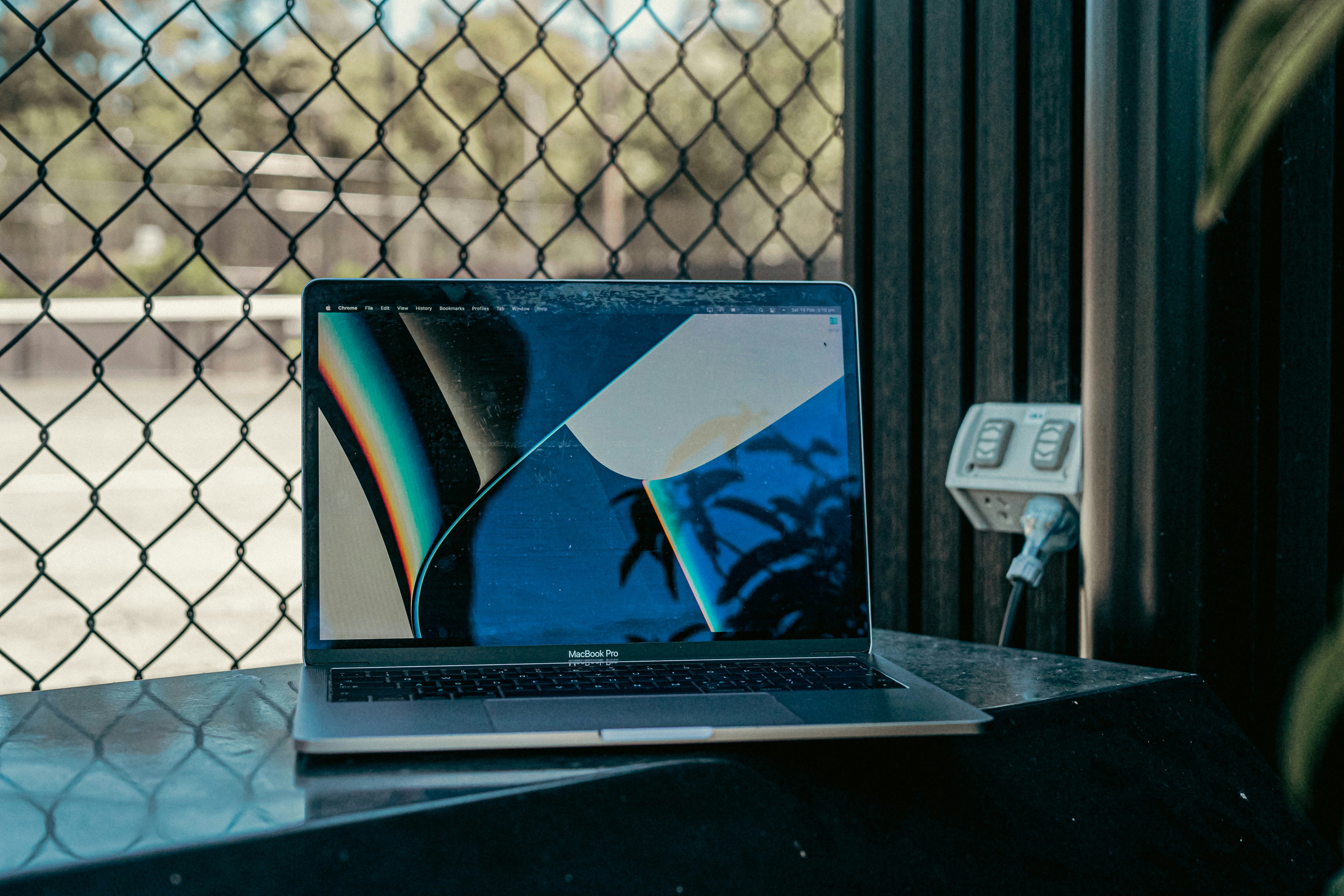 Outdoor Workstation Behind Chain-Link: Neon Reflections on a Laptop Screen