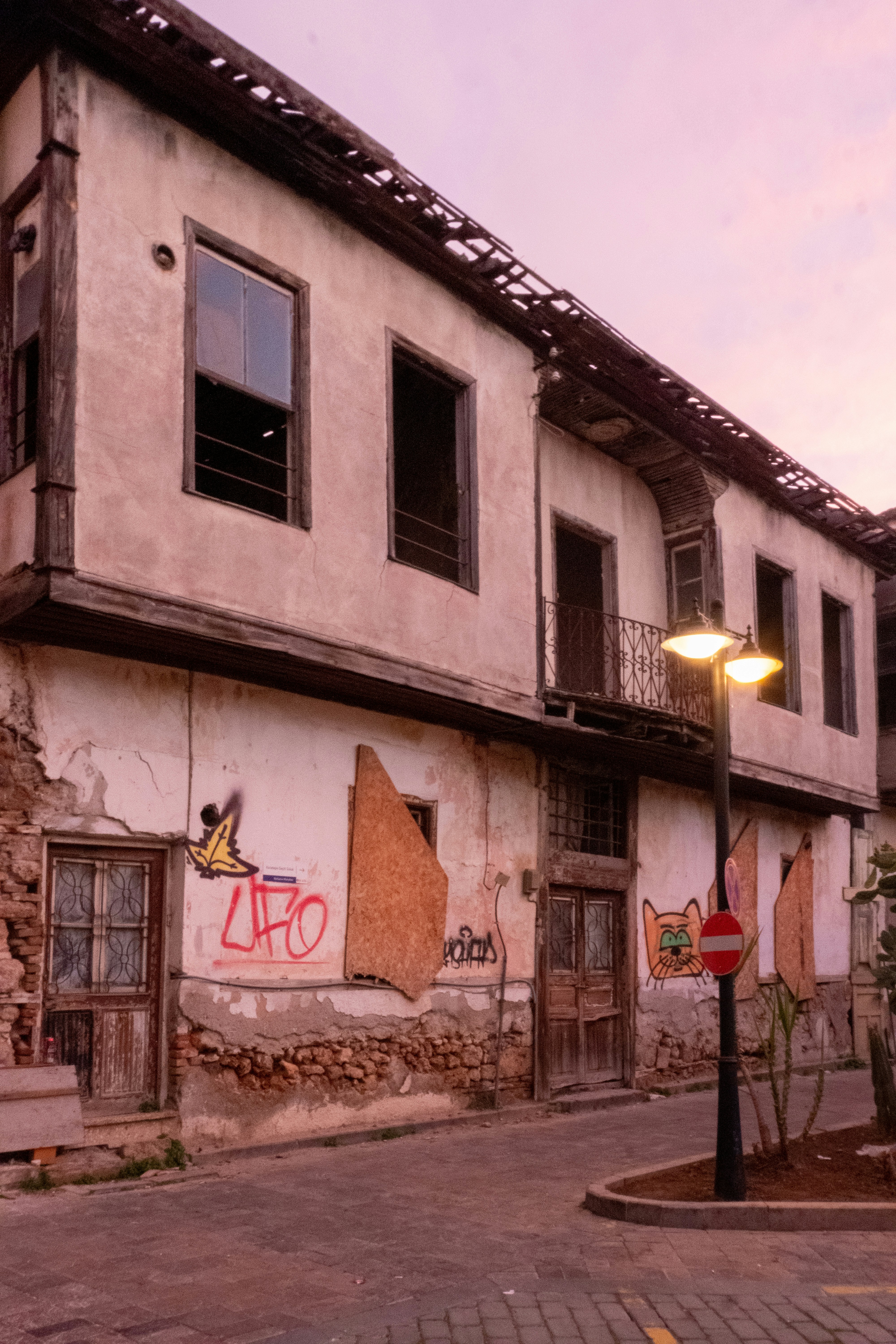 Abandoned building with boarded windows and vibrant graffiti, set against a twilight sky. Street lamp illuminates the scene, enhancing the atmosphere of neglect and artistry.