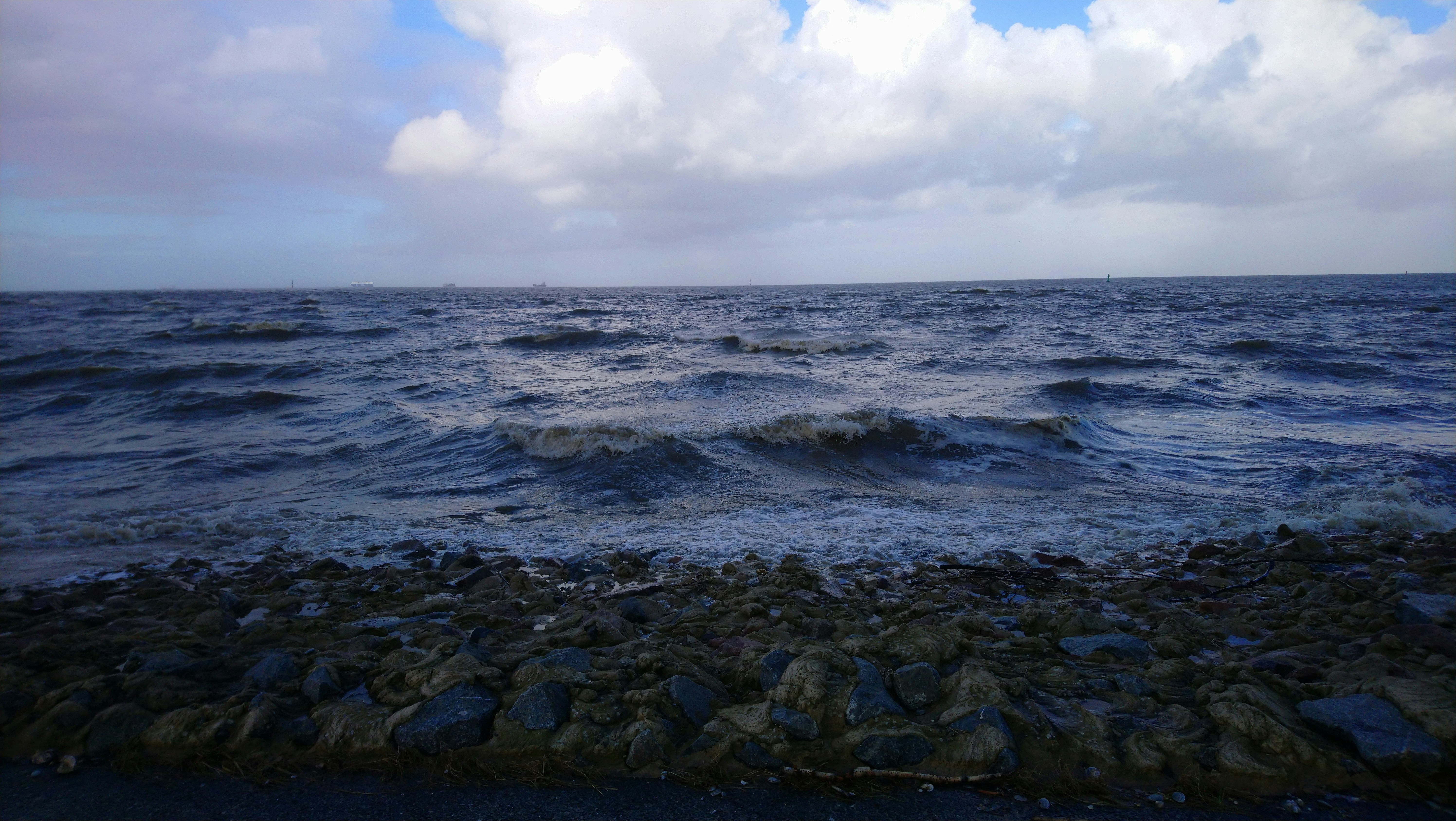 Choppy waves crashing against a rocky shoreline under a partly cloudy sky.