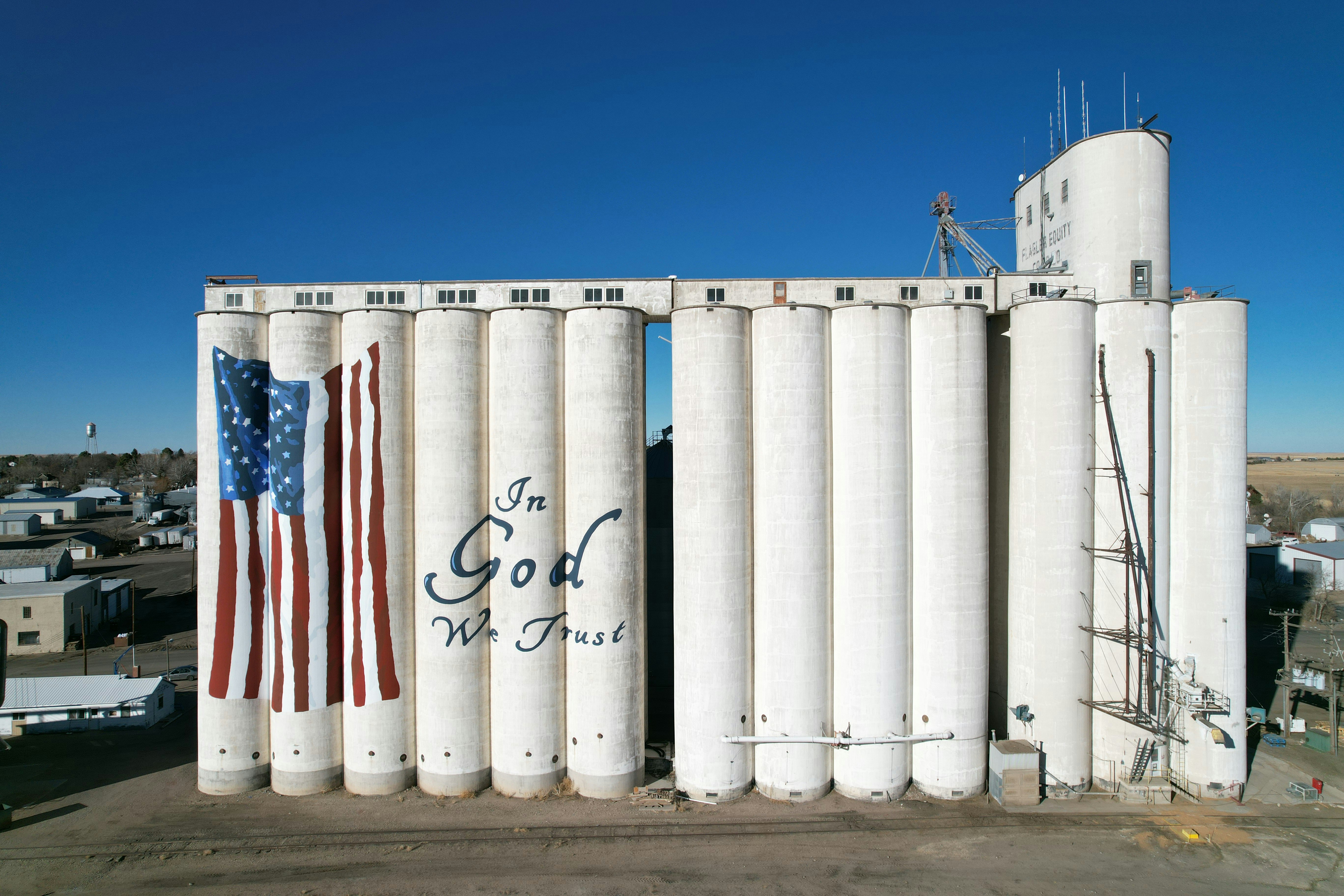 Silo structure adorned with a large mural featuring the American flag and the phrase 'In God We Trust'.