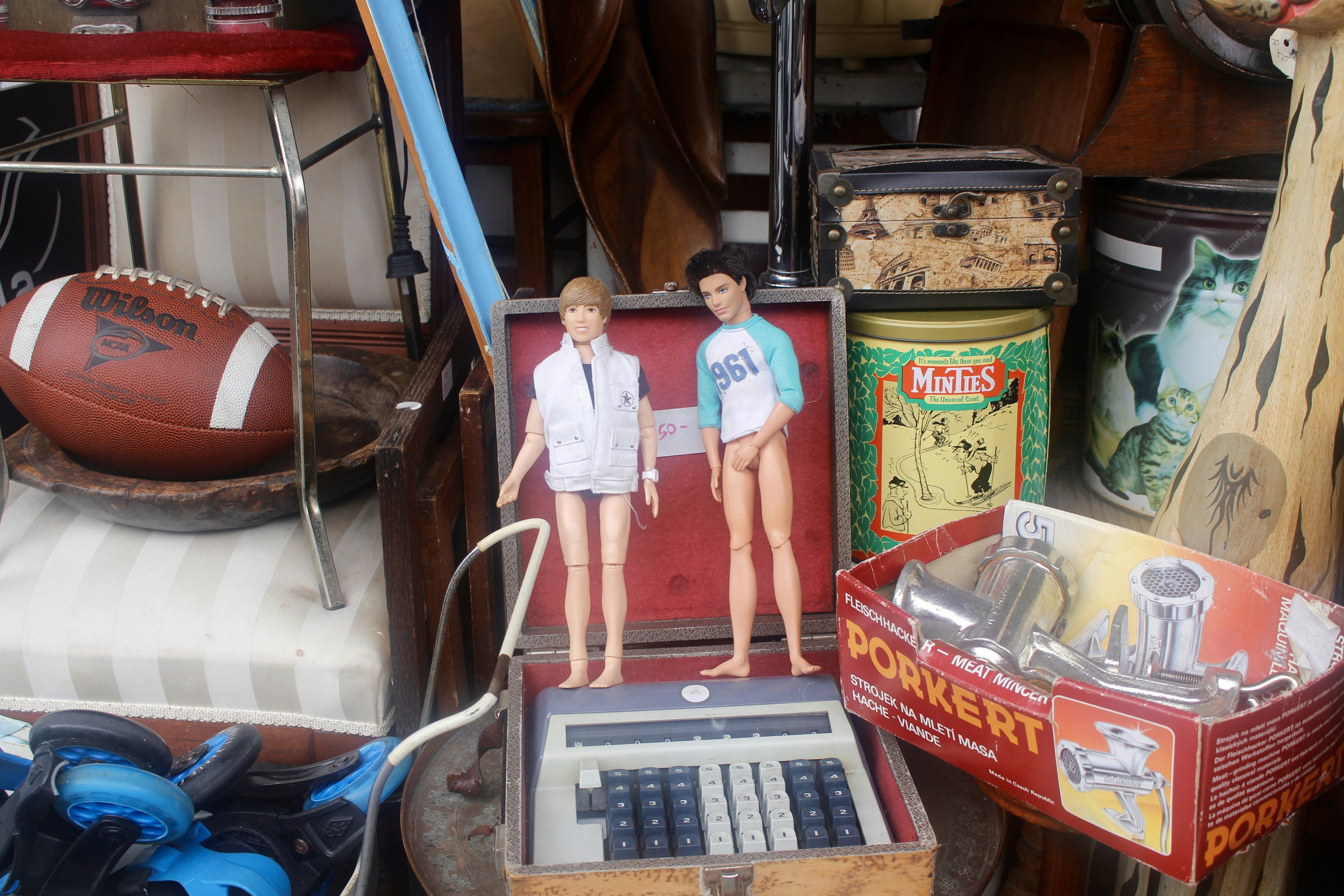 Two vintage action figures stand beside an old typewriter, surrounded by various retro collectibles. The scene evokes a sense of nostalgia and curiosity.