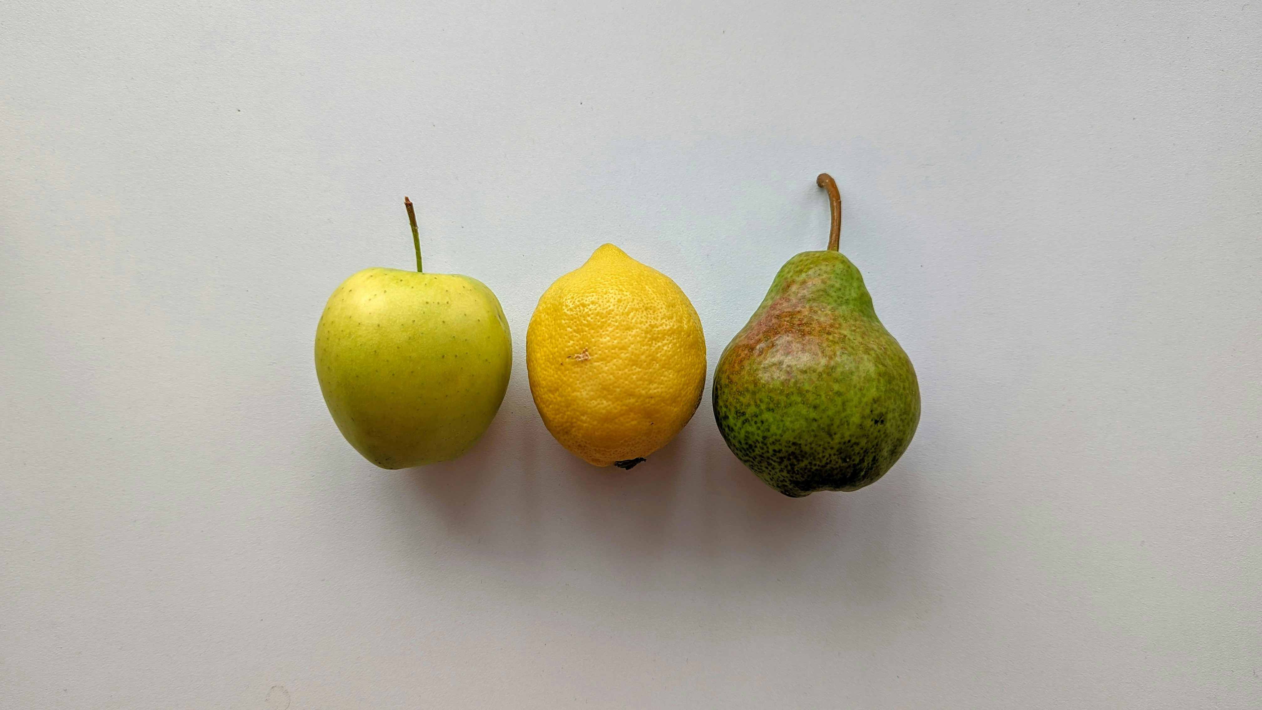 three pears, a lemon and a pear on a white surface
