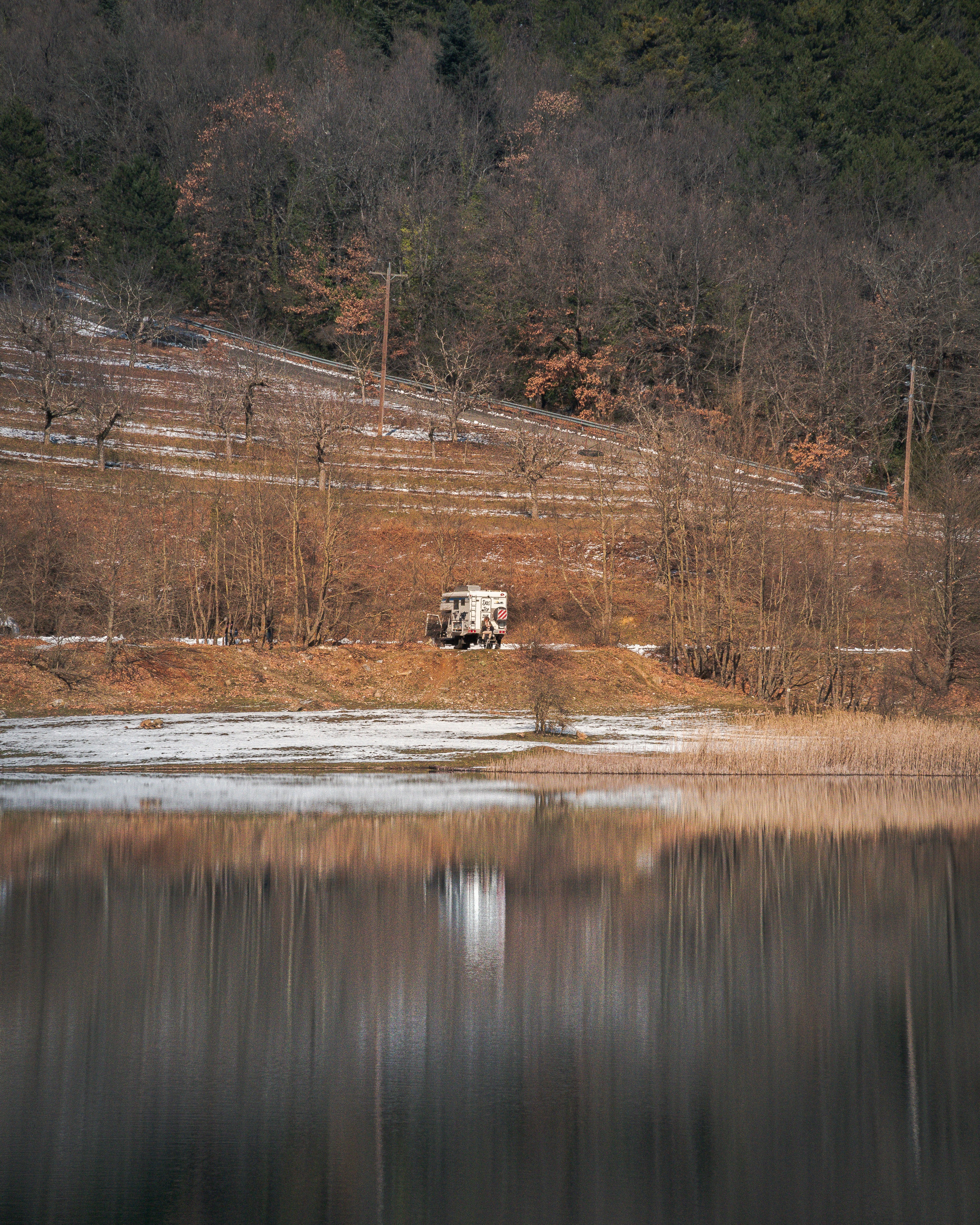 Lakeside Sentinel: a lone utility vehicle guards a frost-kissed shoreline beneath timbered hills