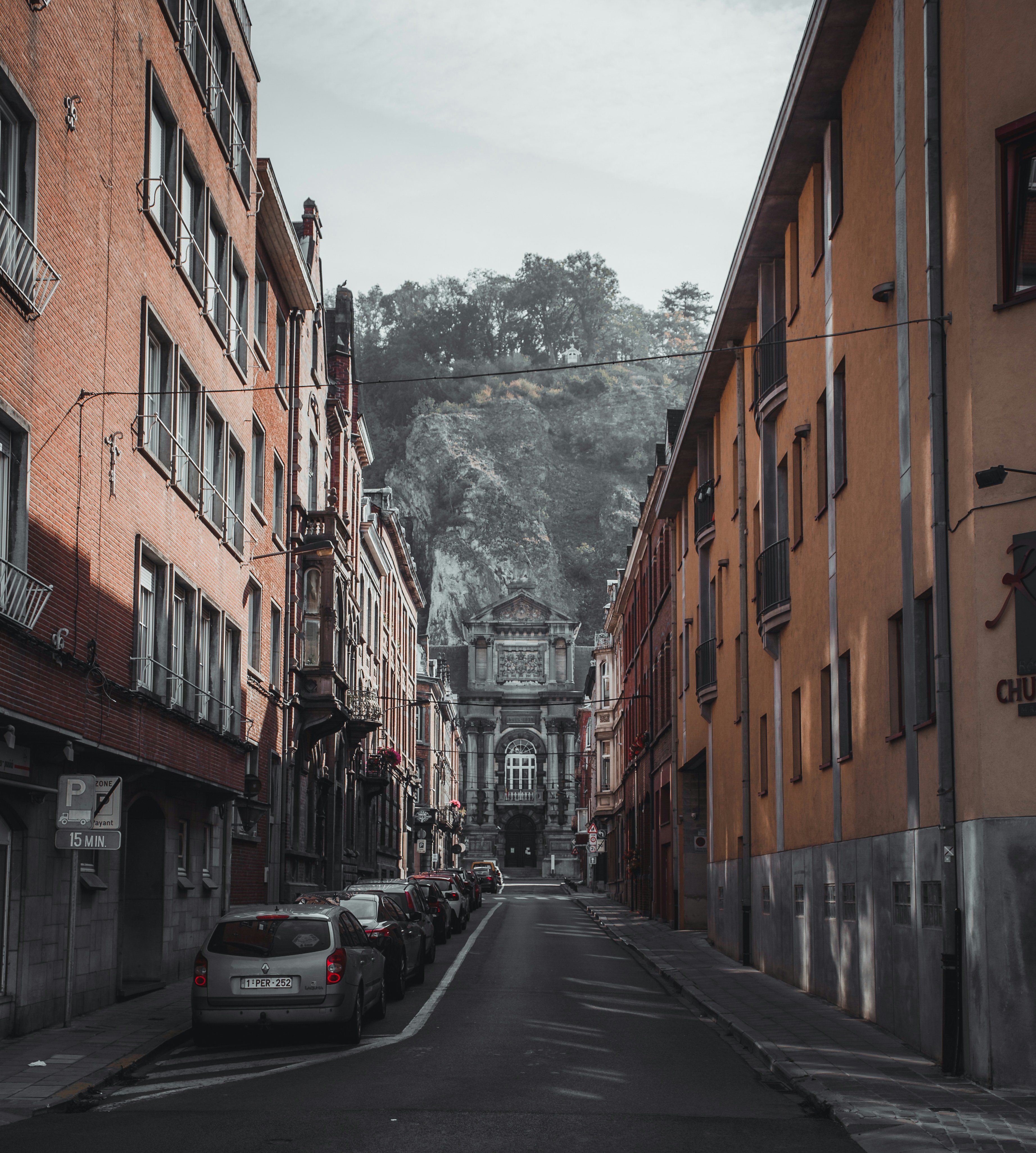 Narrow street flanked by colorful buildings leading toward a historical structure, set against a backdrop of greenery.
