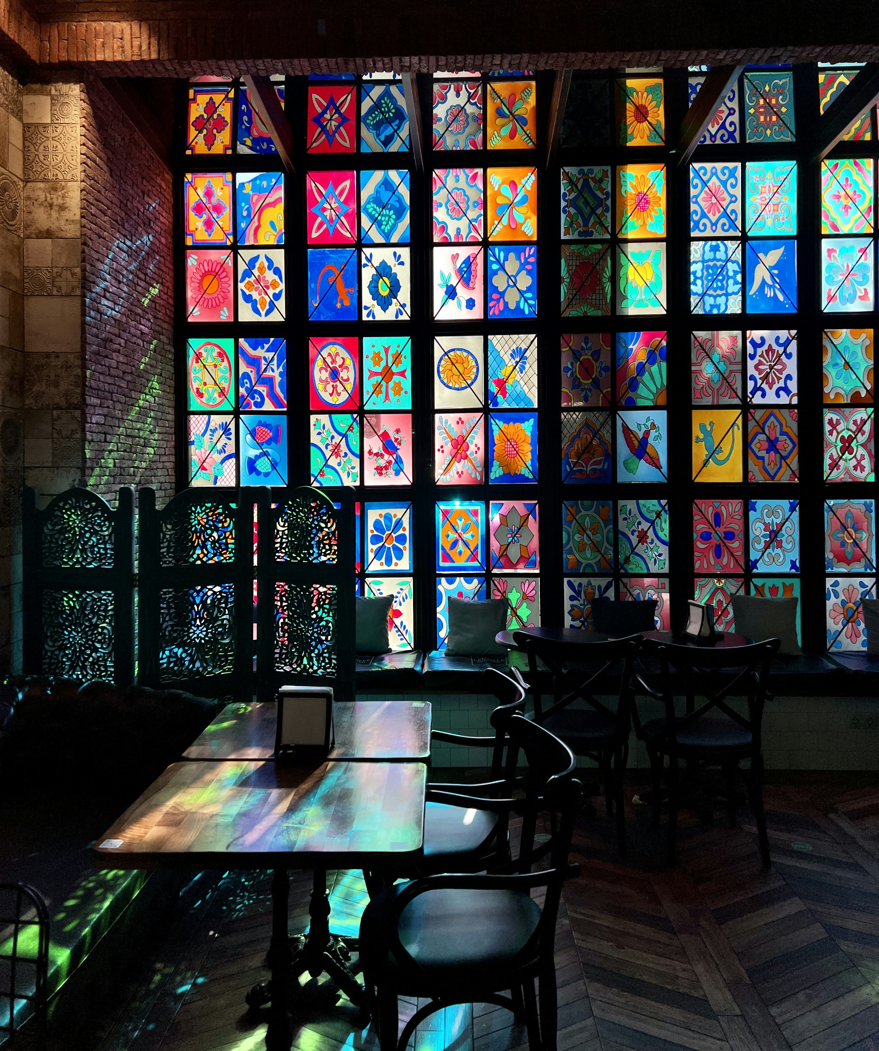 Colorful stained glass windows casting intricate patterns of light across a cozy dining area. The interplay of colors creates a warm and inviting atmosphere.