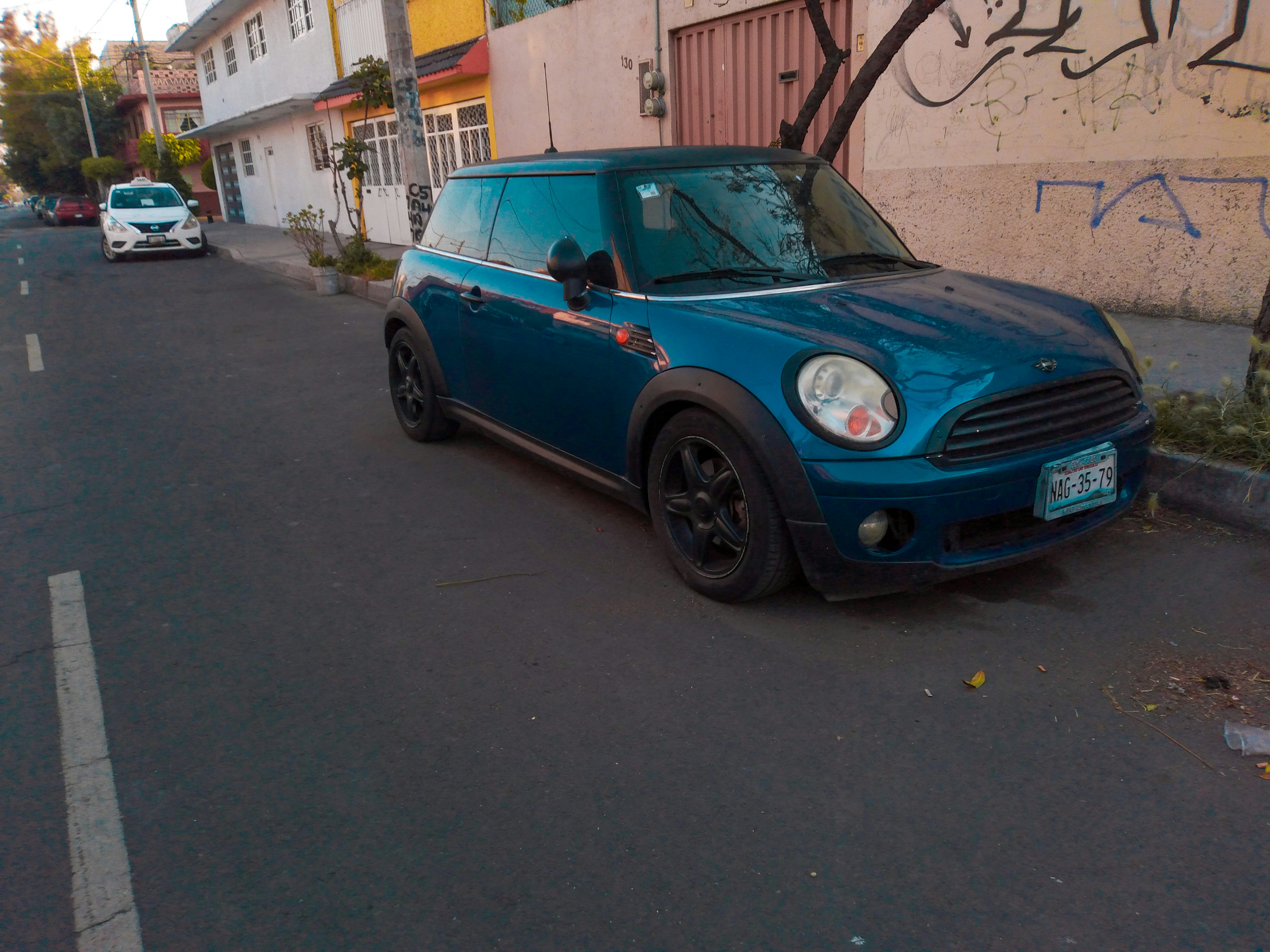 Blue Mini Cooper parked on a quiet urban street lined with buildings.