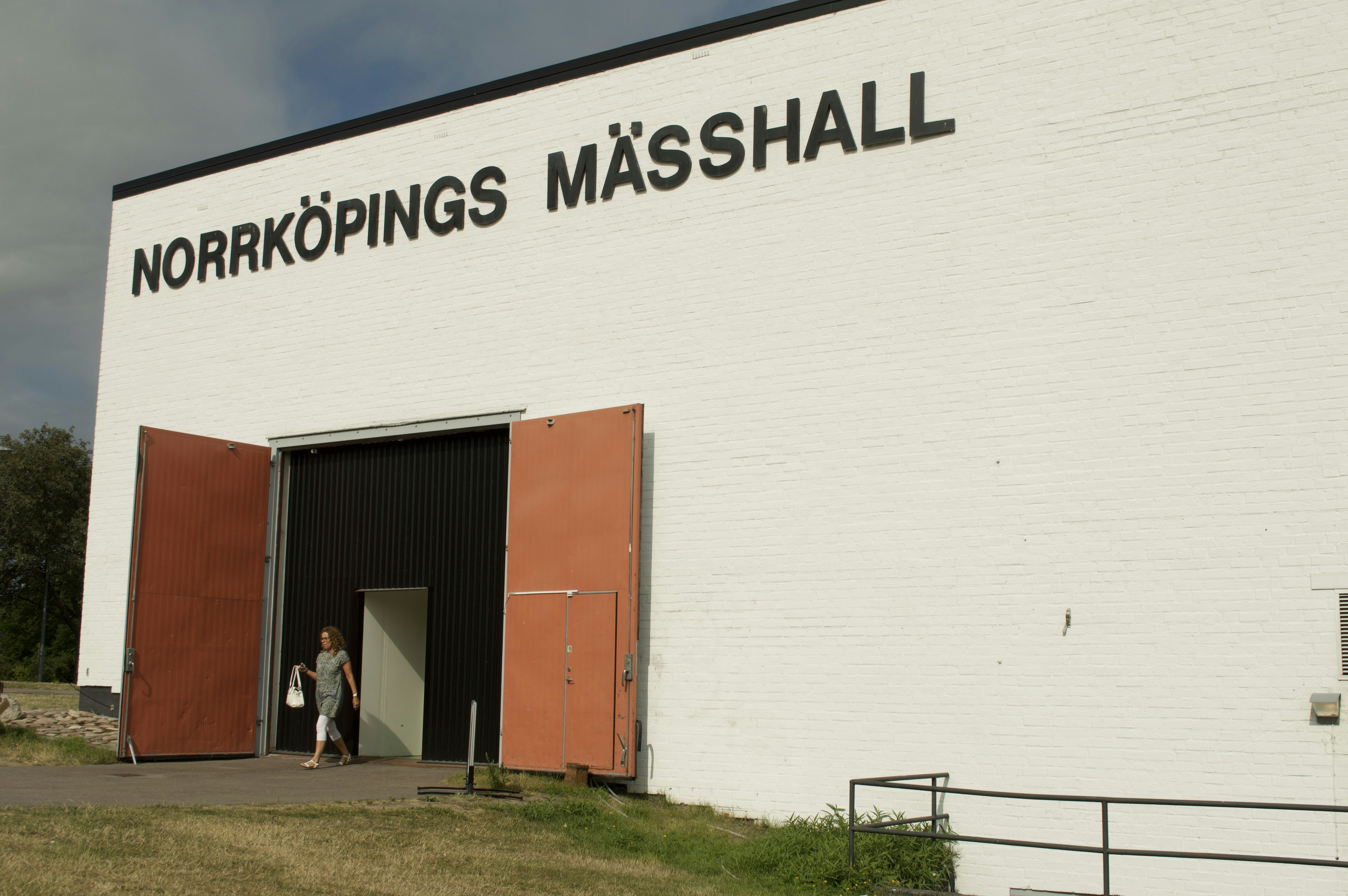 Person walking through an open doorway into a large white building marked 'Norrköpings Mässhall'.