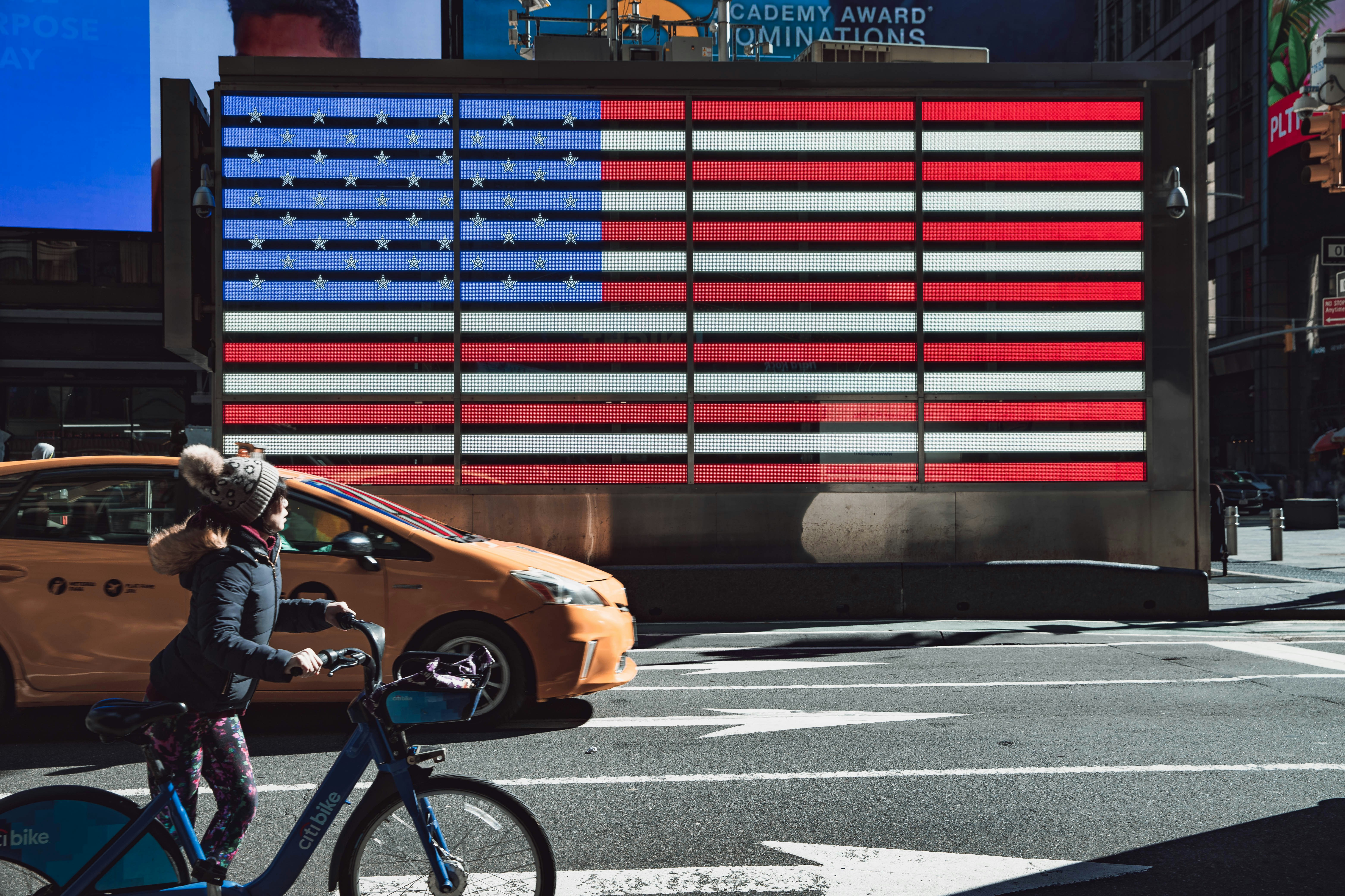 Crossing Lives: A Cyclist Passes the American Flag Billboard