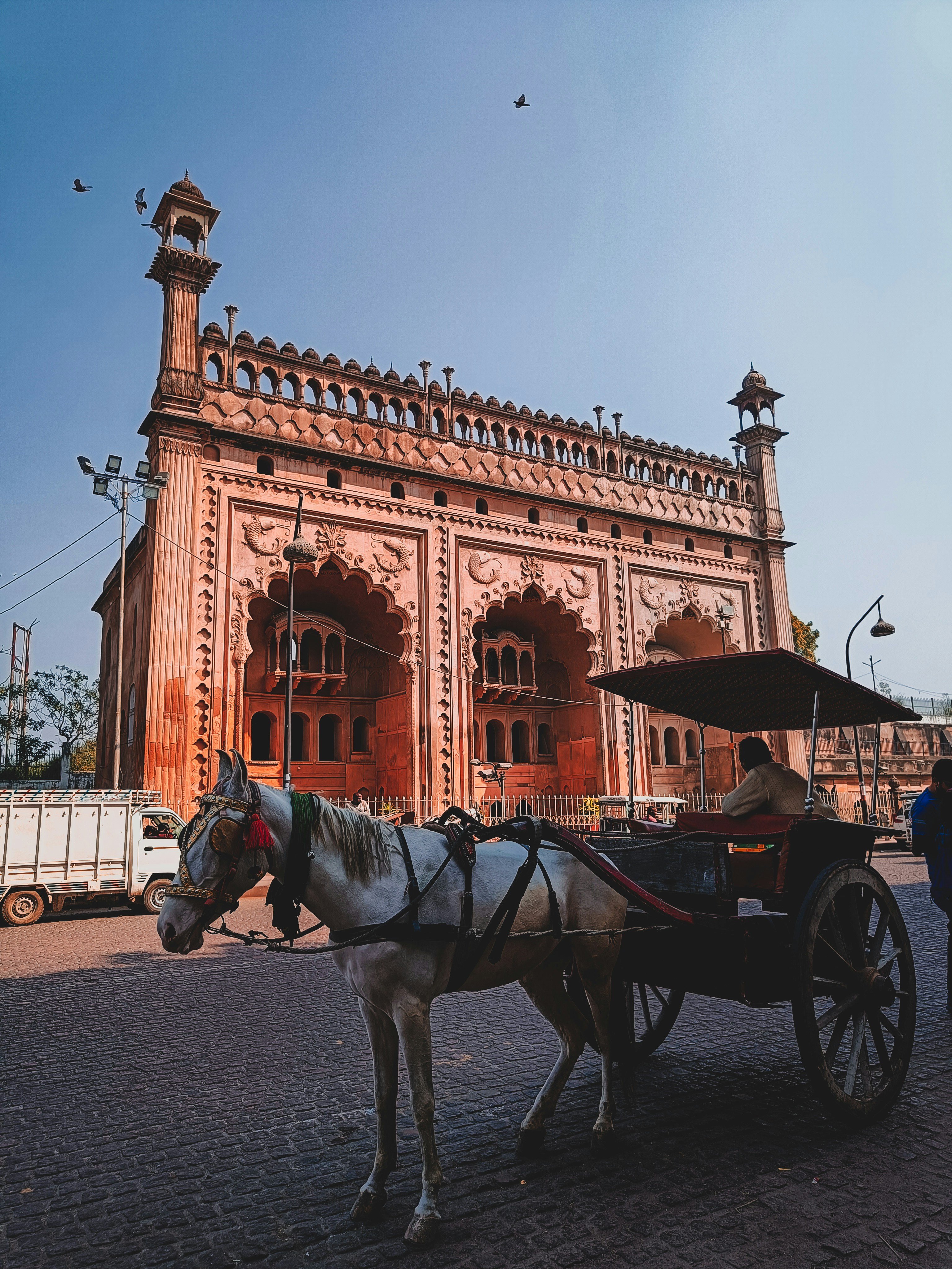 A horse-drawn carriage awaits passengers in front of a grand historical gateway adorned with intricate carvings. The scene captures a blend of tradition and daily life.